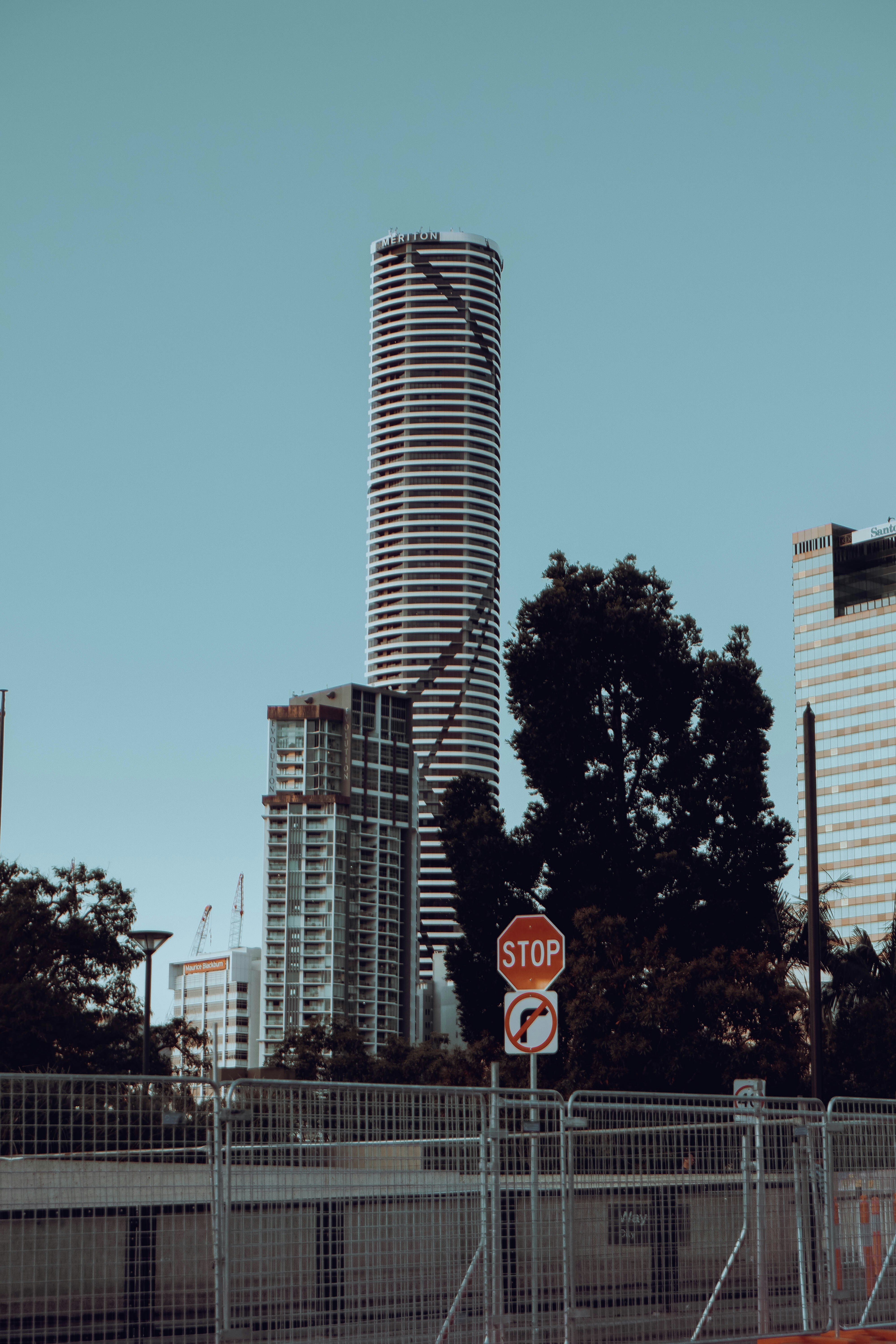 Tall, spiraling skyscraper surrounded by lush trees and construction elements, with a prominent stop sign in the foreground.