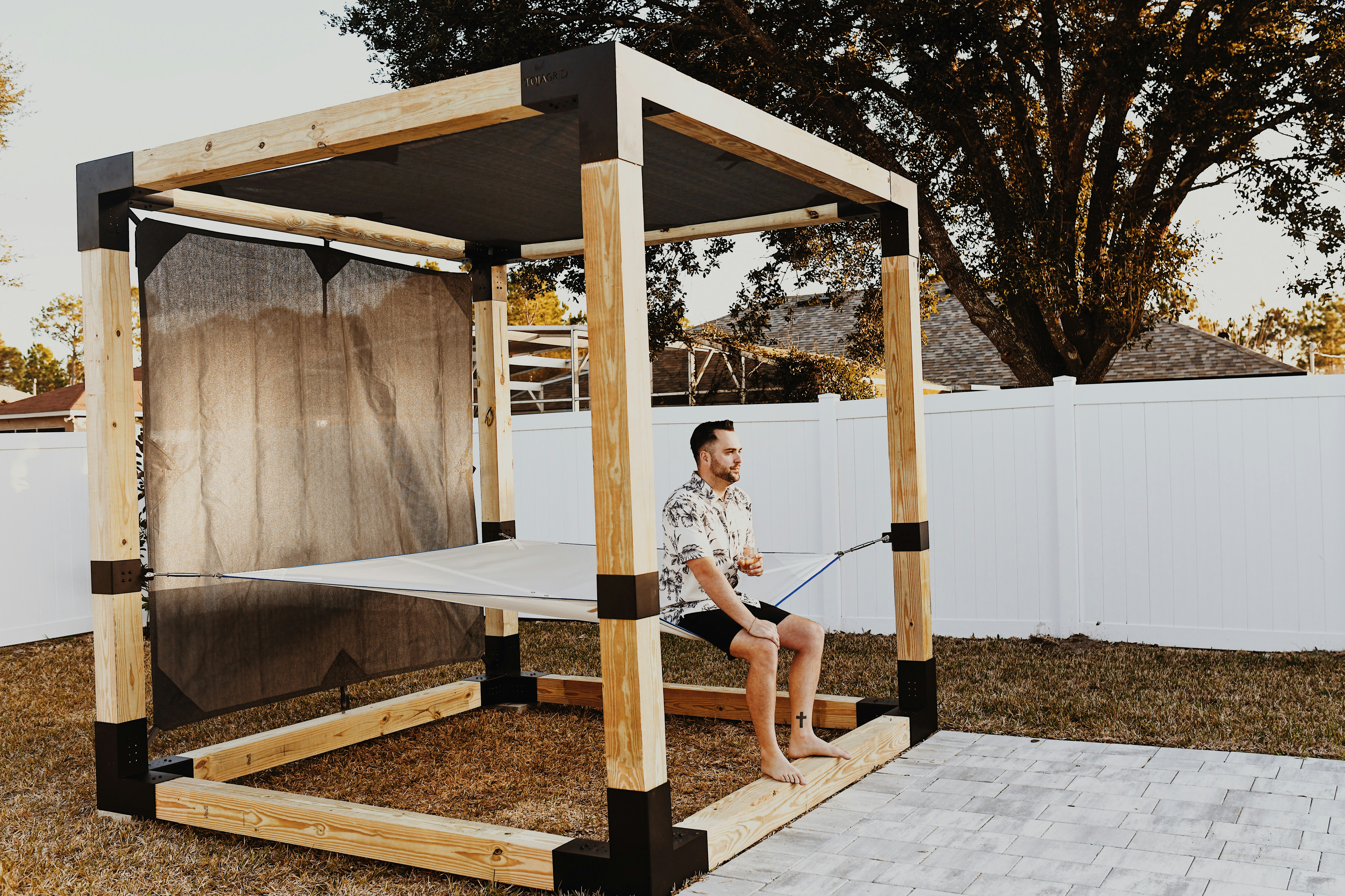 Man seated on a modern wooden gazebo platform in a suburban yard