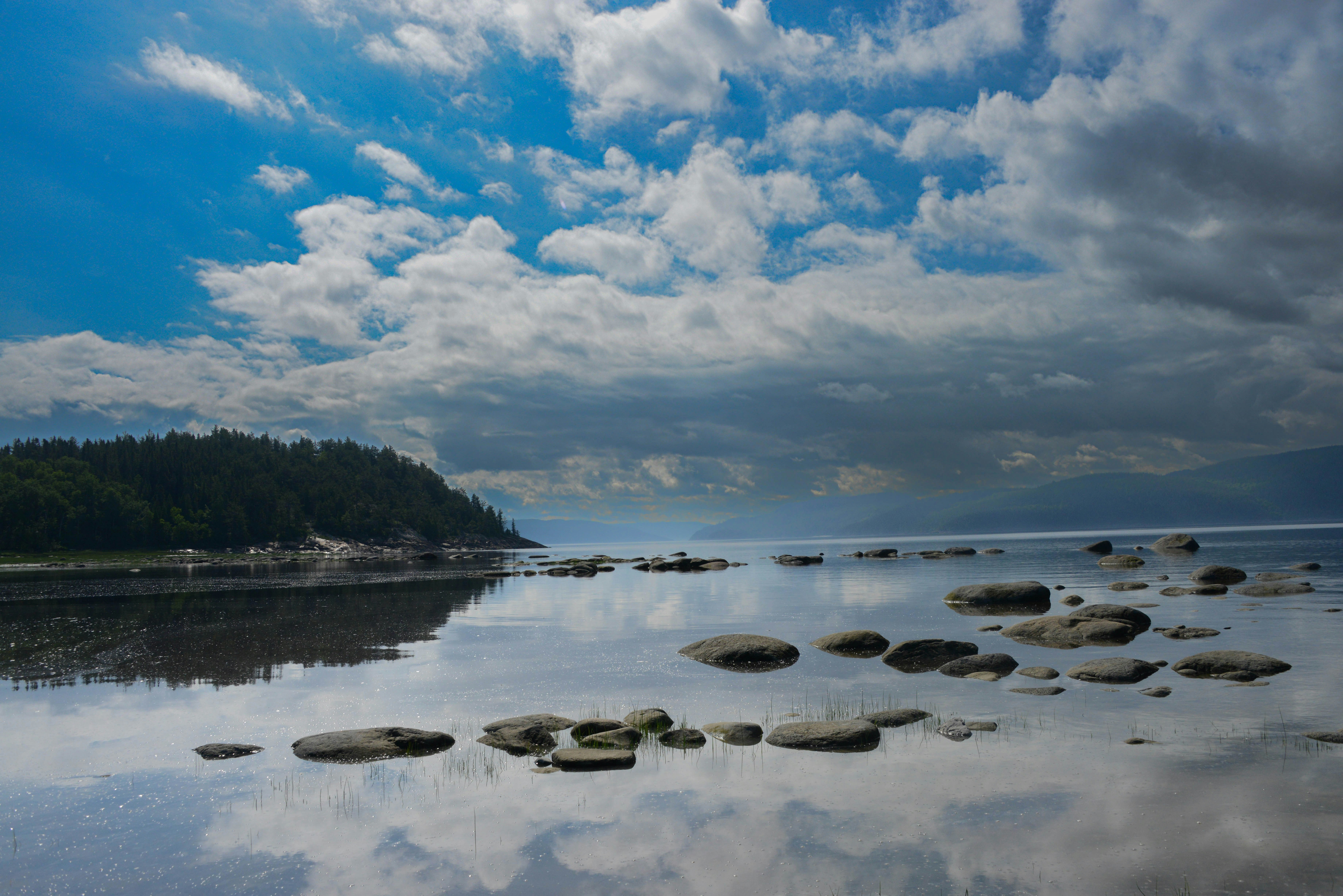 A body of water surrounded by rocks and trees photo – Free Water Image ...