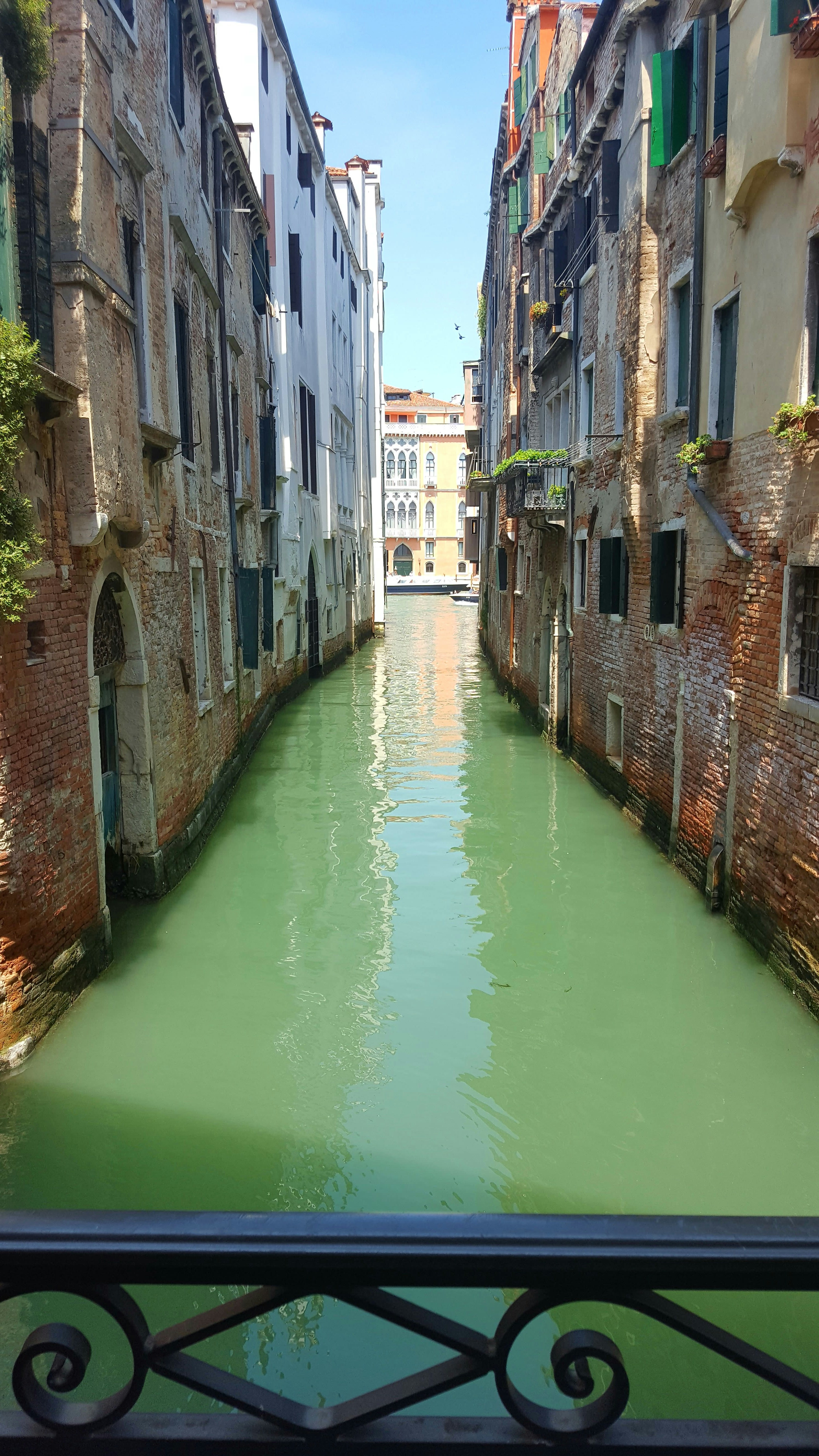 Narrow canal flanked by aged brick buildings in Venice, reflecting vibrant colors of the architecture on the water's surface.