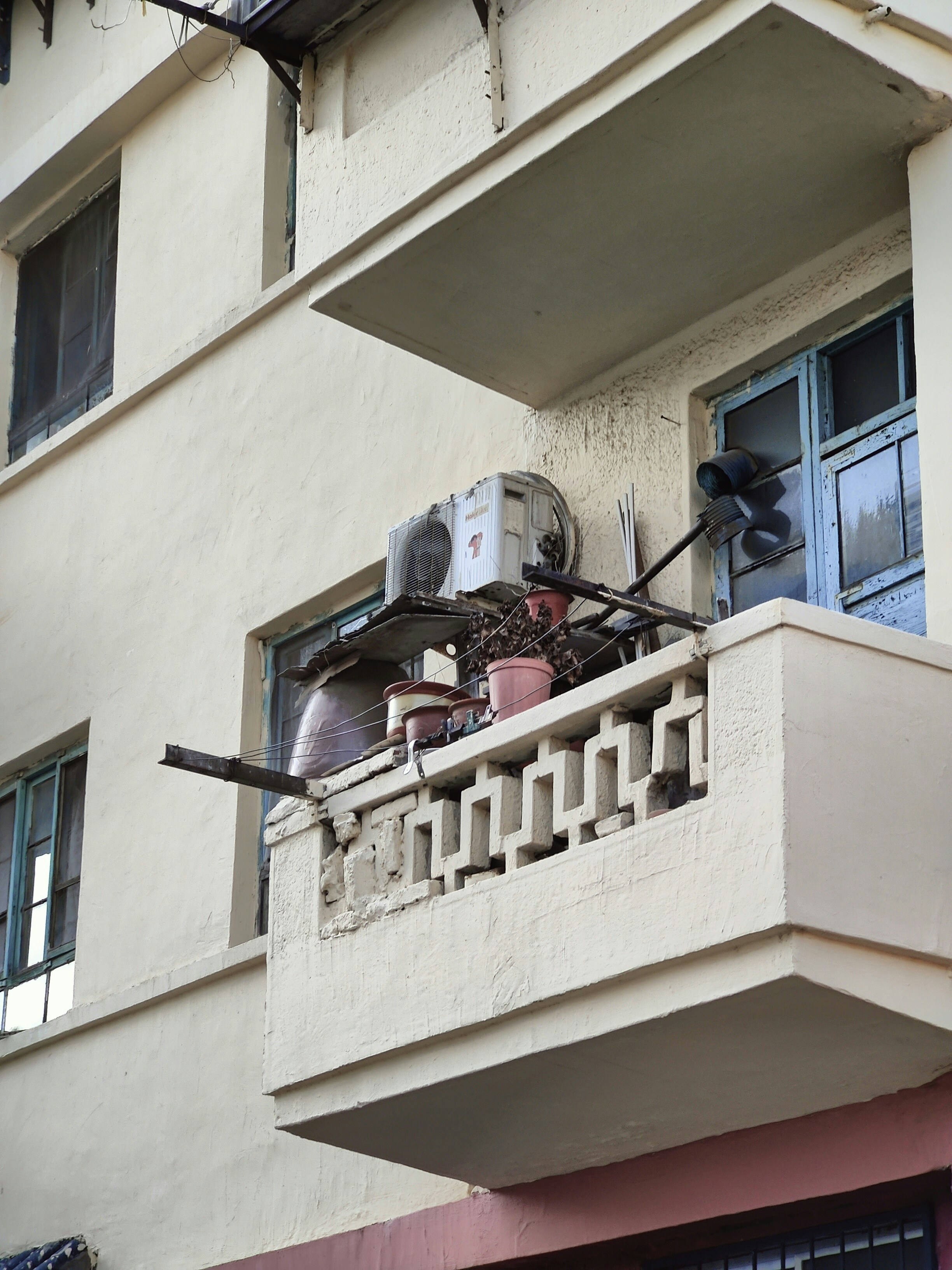 An urban balcony featuring an air conditioning unit and potted plants, showcasing the blend of utility and personal touch in city living.