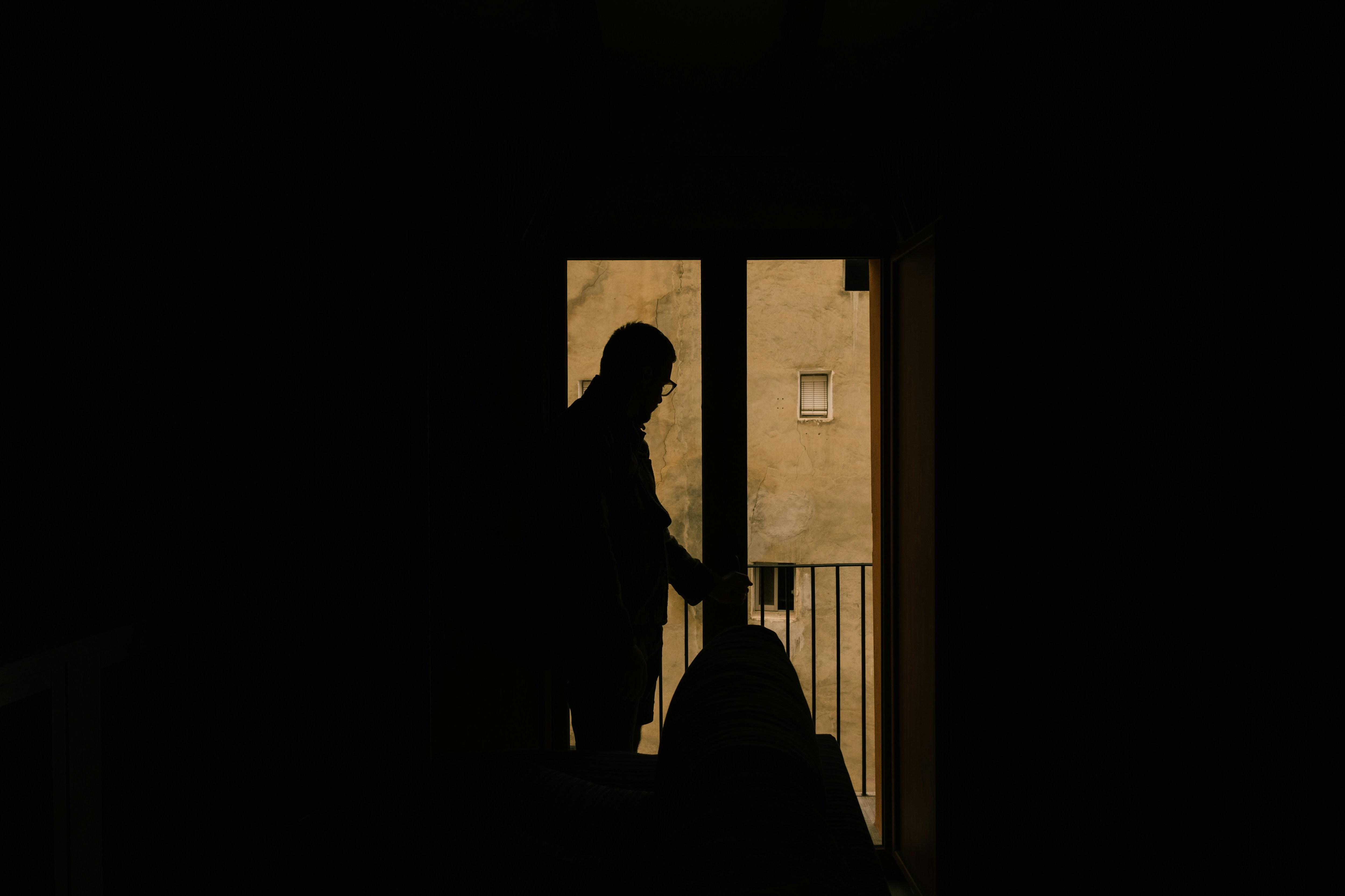 A young man standing next to a window in the dark.