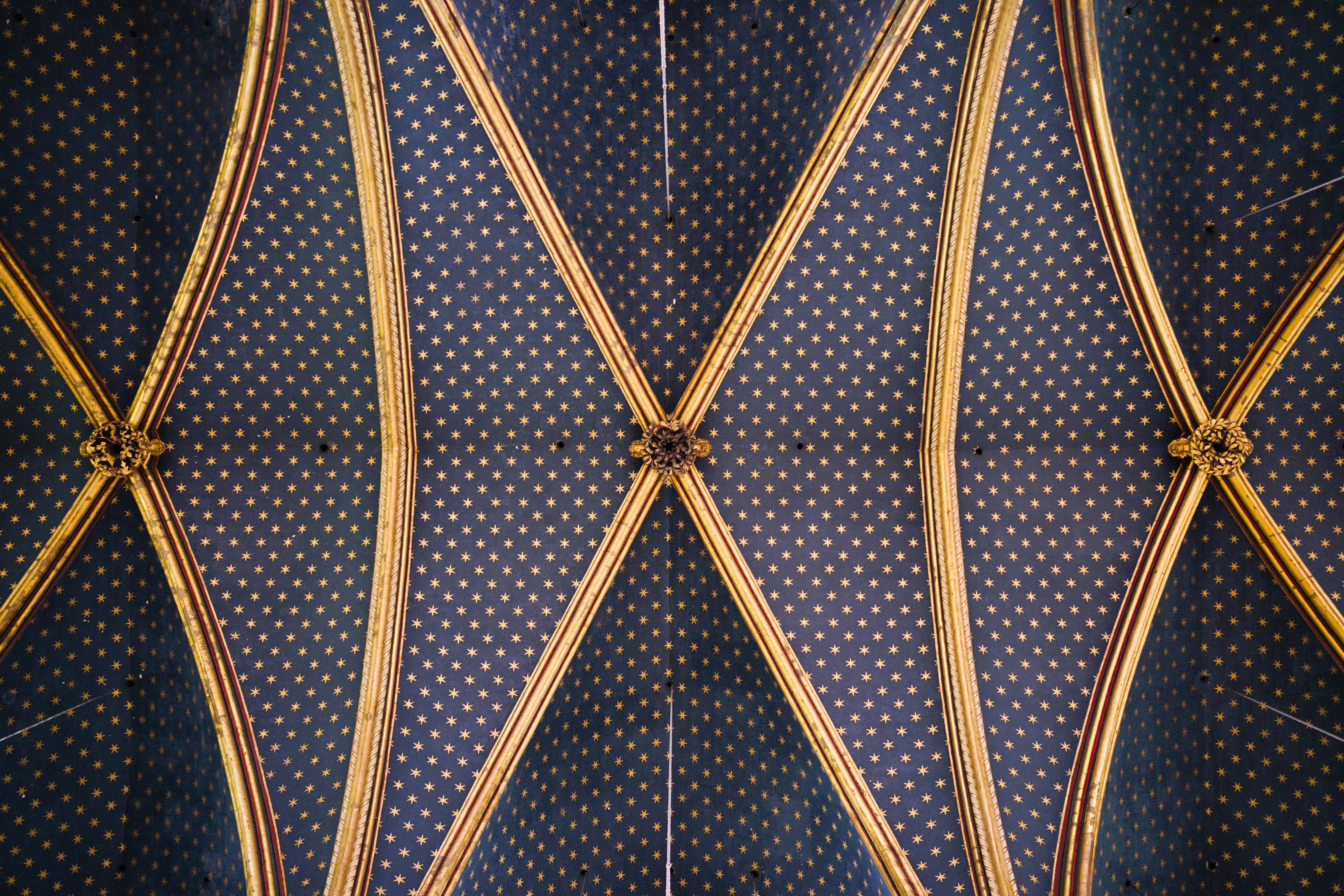 Intricate ceiling design showcasing a pattern of gold and blue with symmetrical arches and dotted embellishments.