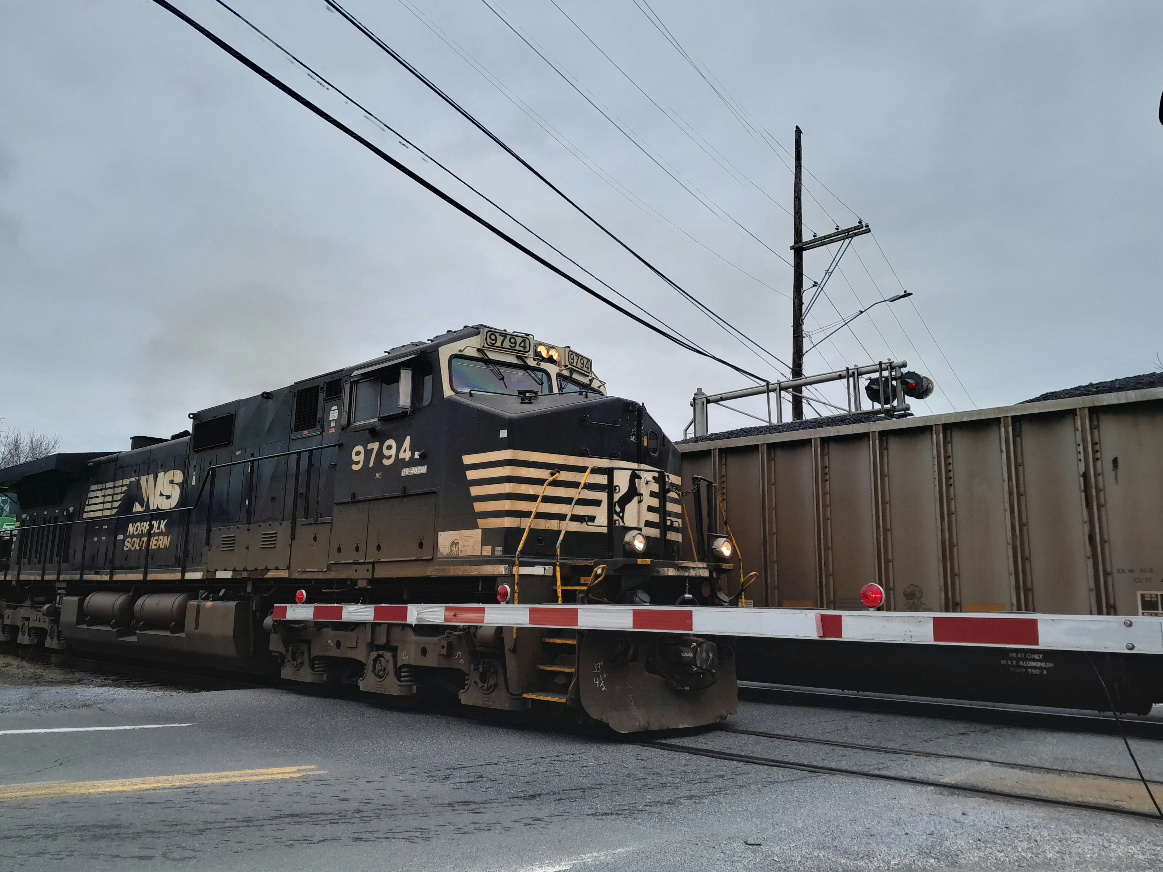 Freight train passing a railroad crossing under a cloudy sky.