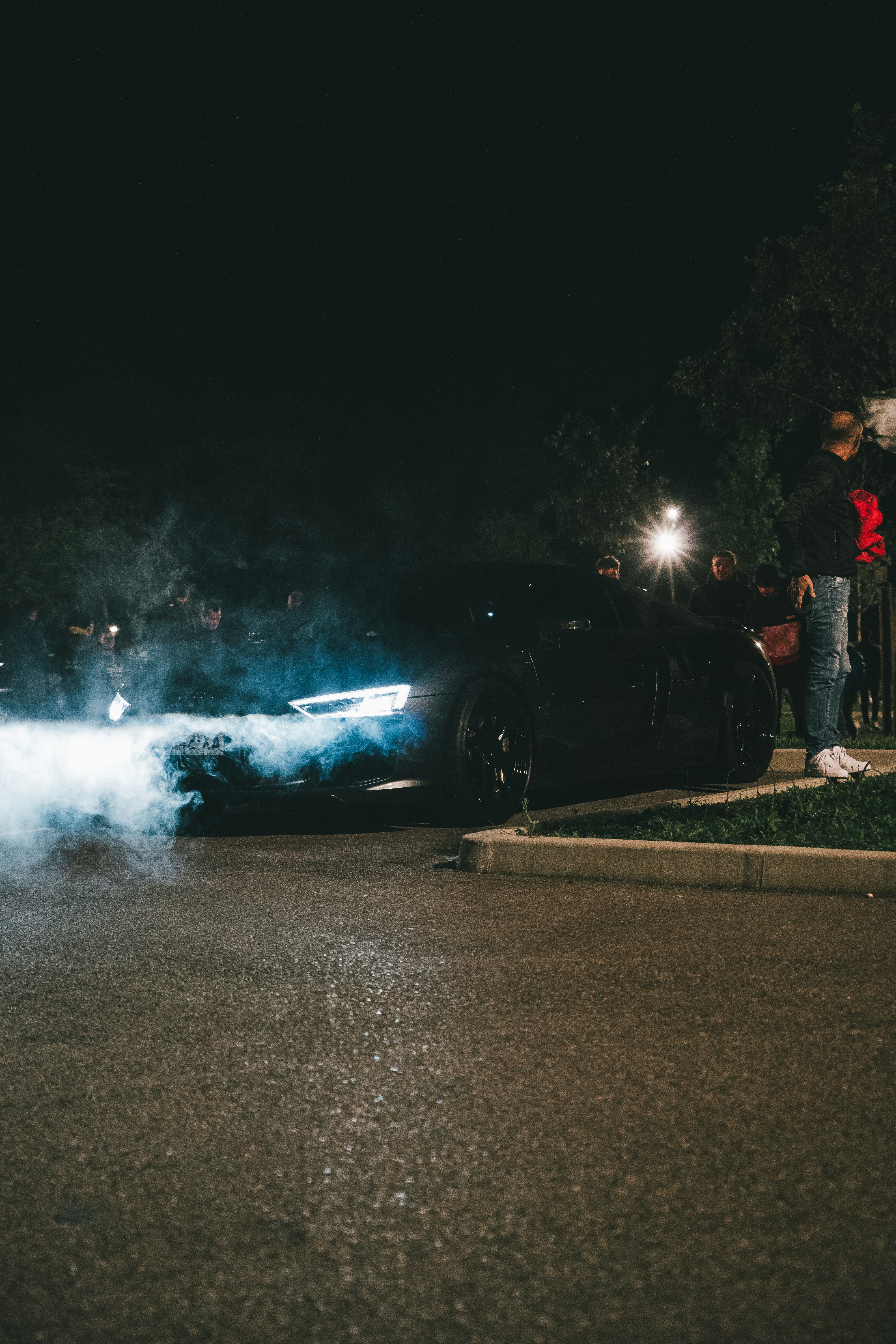 Midnight Drift: Smoke, Headlights, and a Sleek Black Sports Car Among Nighttime Onlookers
