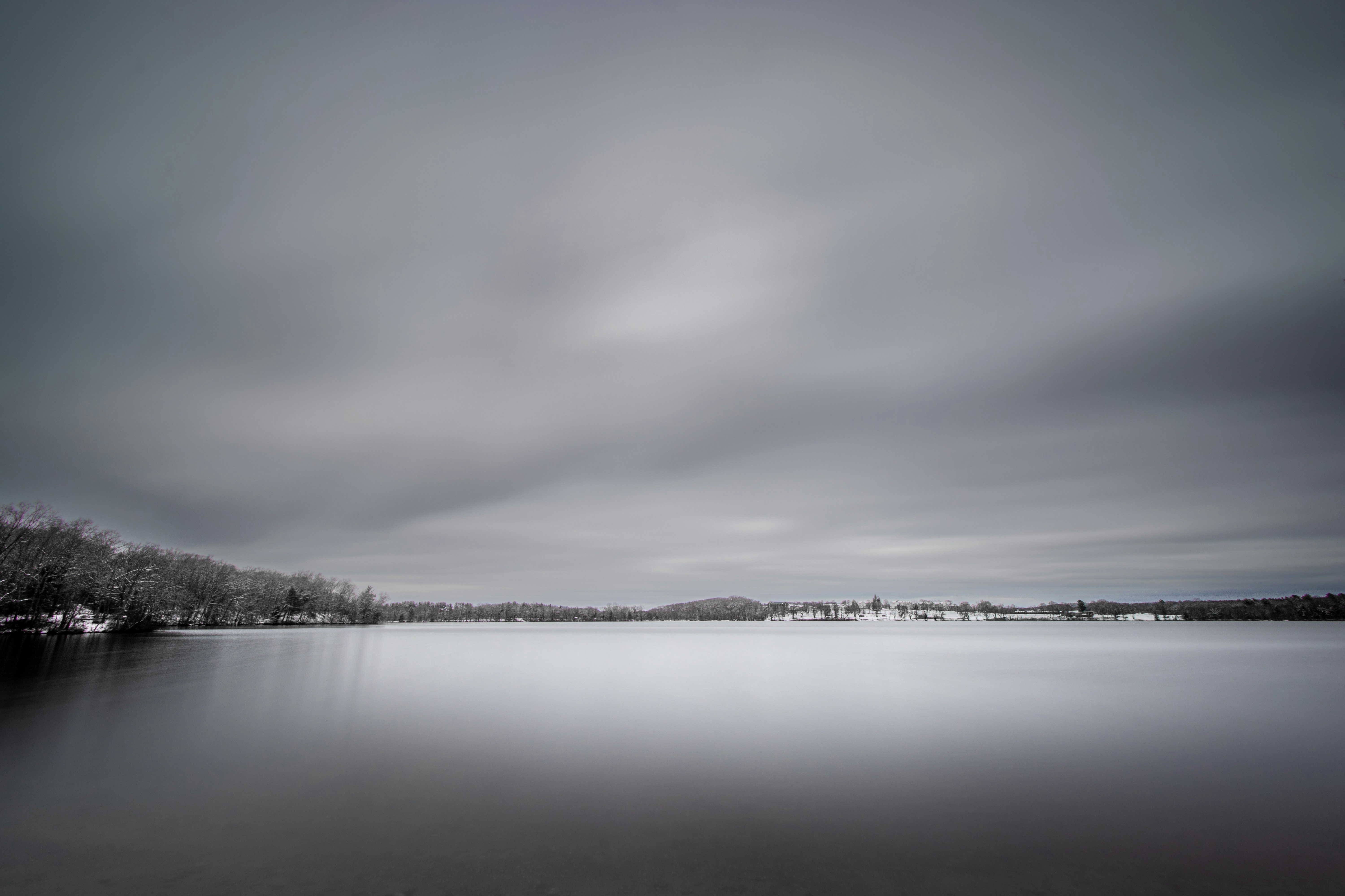 Long exposure flattens Chauncy Lake, reflecting the cloudy sky and surrounding trees. | a large body of water surrounded by trees