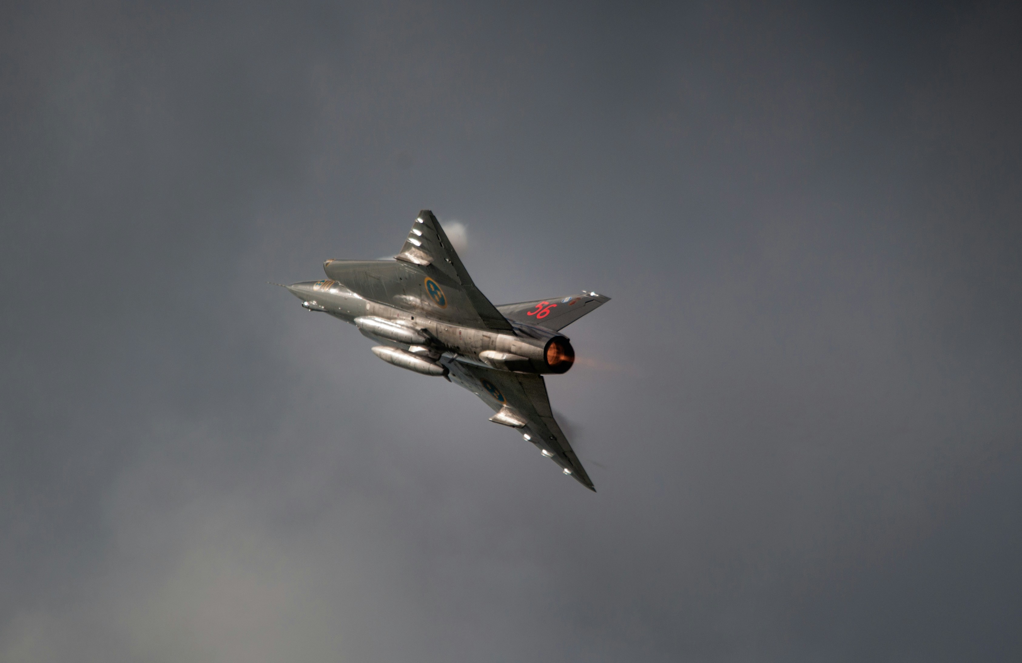 Military jet maneuvering through cloudy skies with afterburners ignited.
