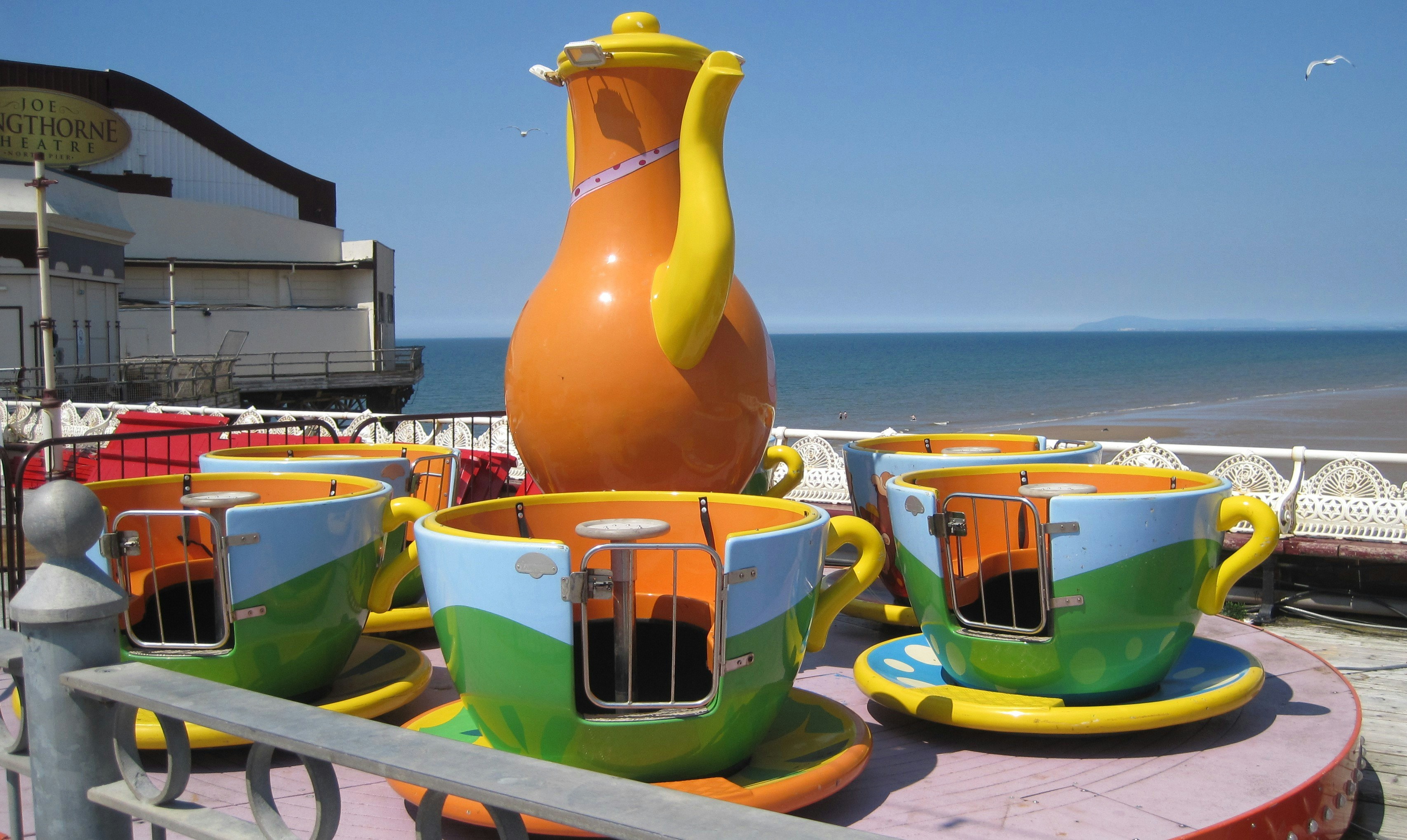 Colorful teacup ride by the sea under a clear blue sky.