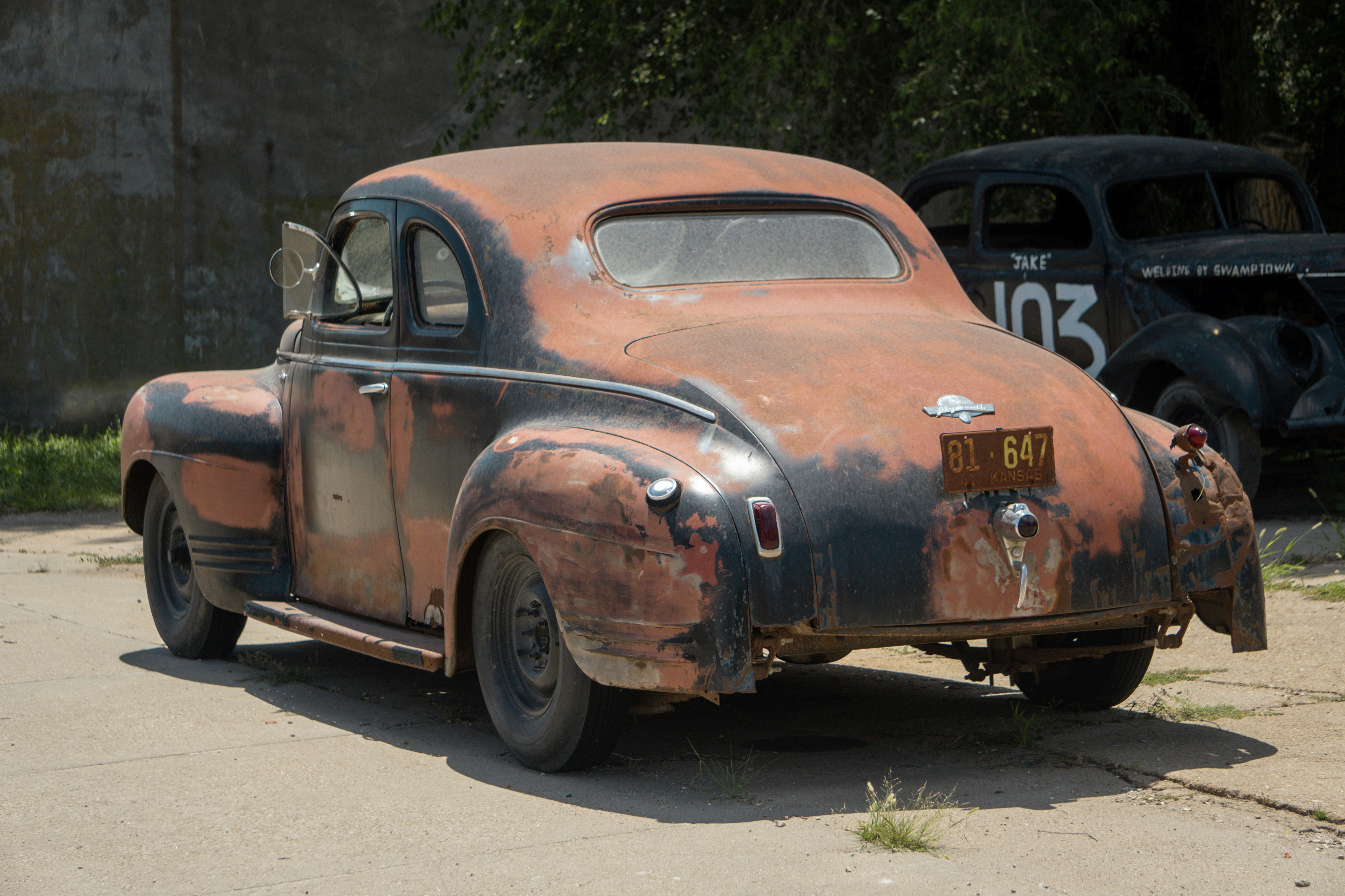 Vintage car with a weathered exterior parked on a sunlit street, showcasing its rich history and character.