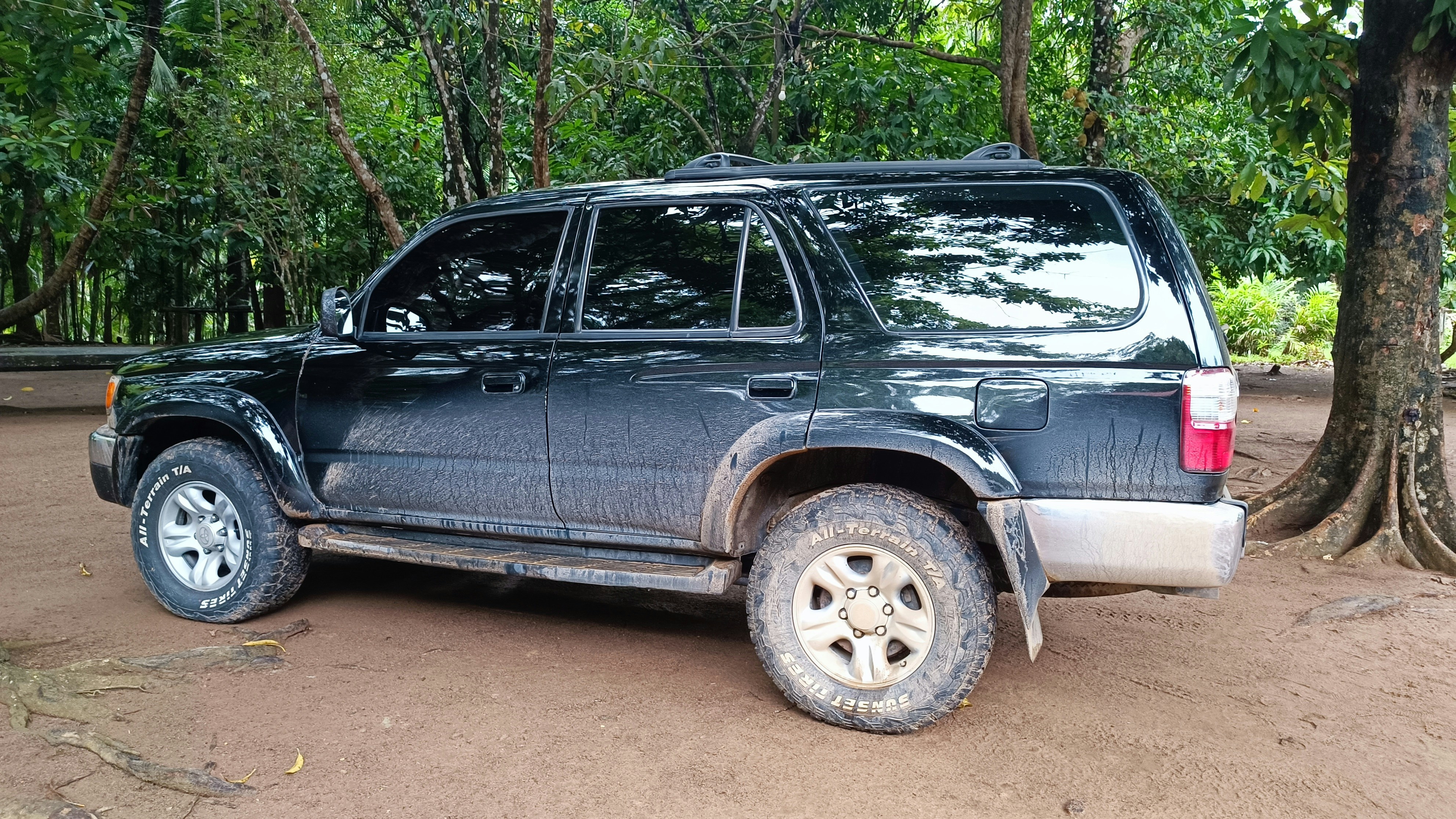 Dark blue SUV parked on a dirt lot with a forest backdrop. Mud-splattered tires emphasize its off-road readiness.