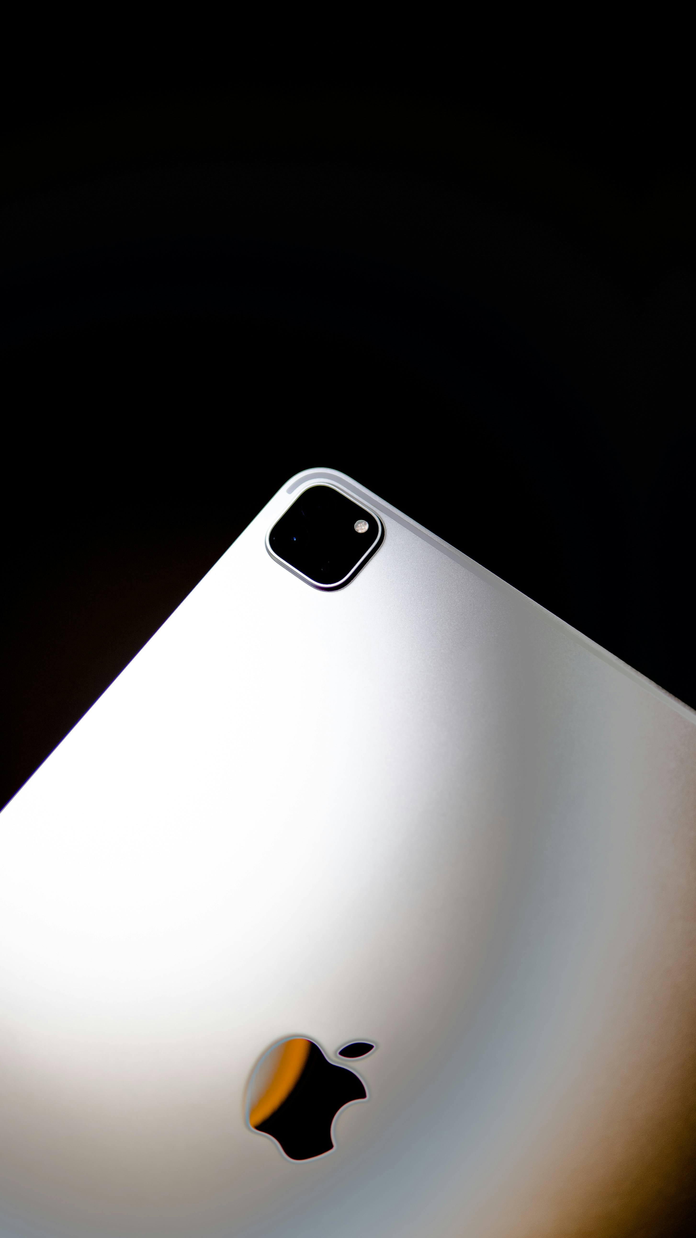 floating silver iPad Pro dark background | a close up of the back of an iphone