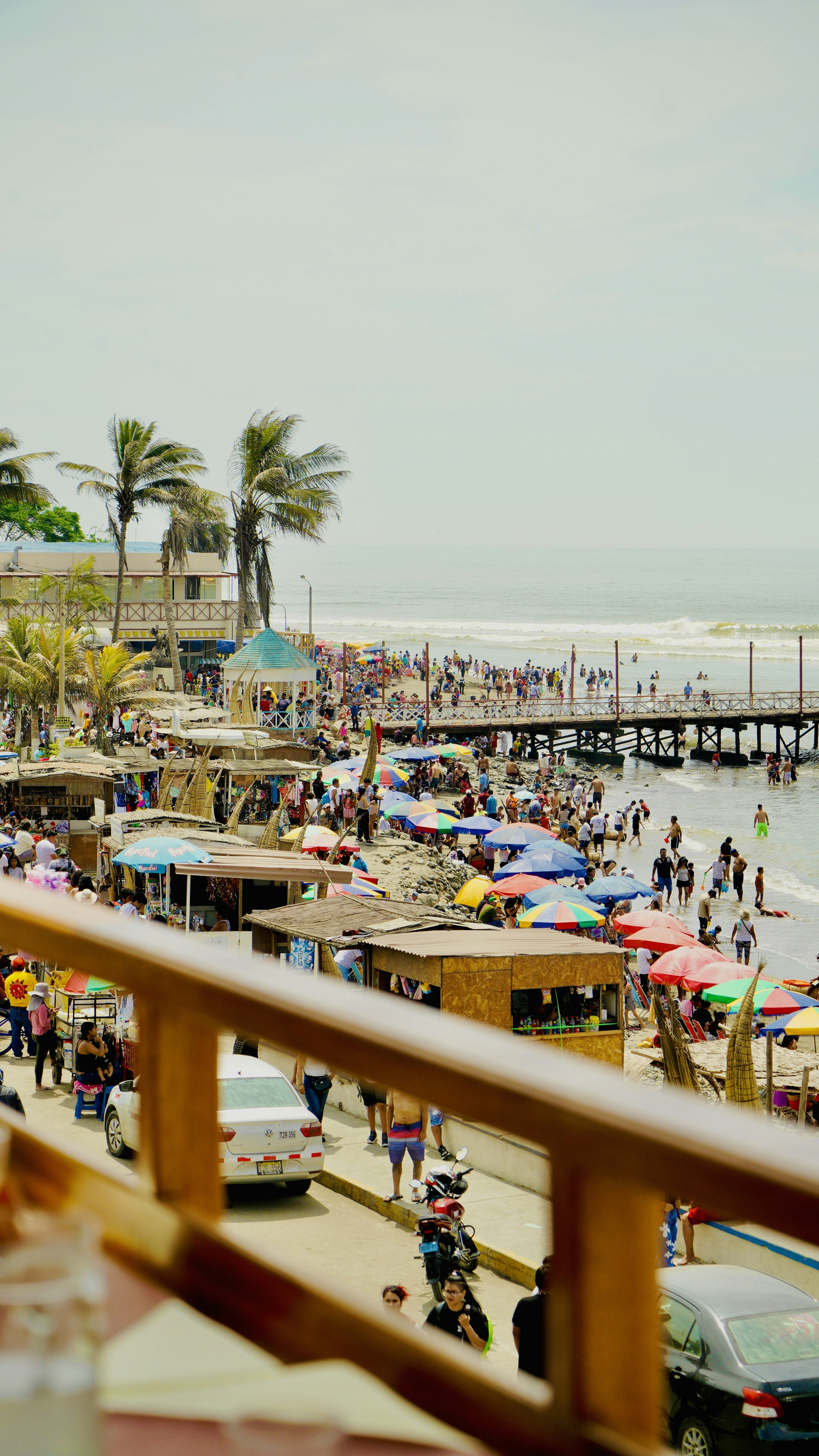 Umbrella Parade Along a Bustling Palm-Fringed Beach and Pier