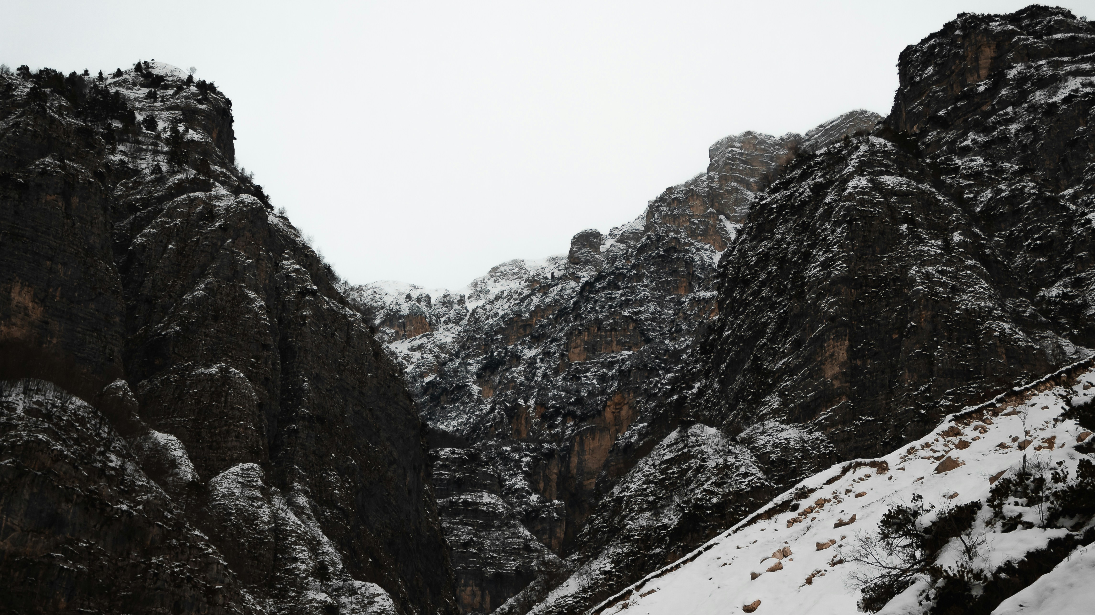 Snow-dusted rocky cliffs rise sharply under a pale sky.