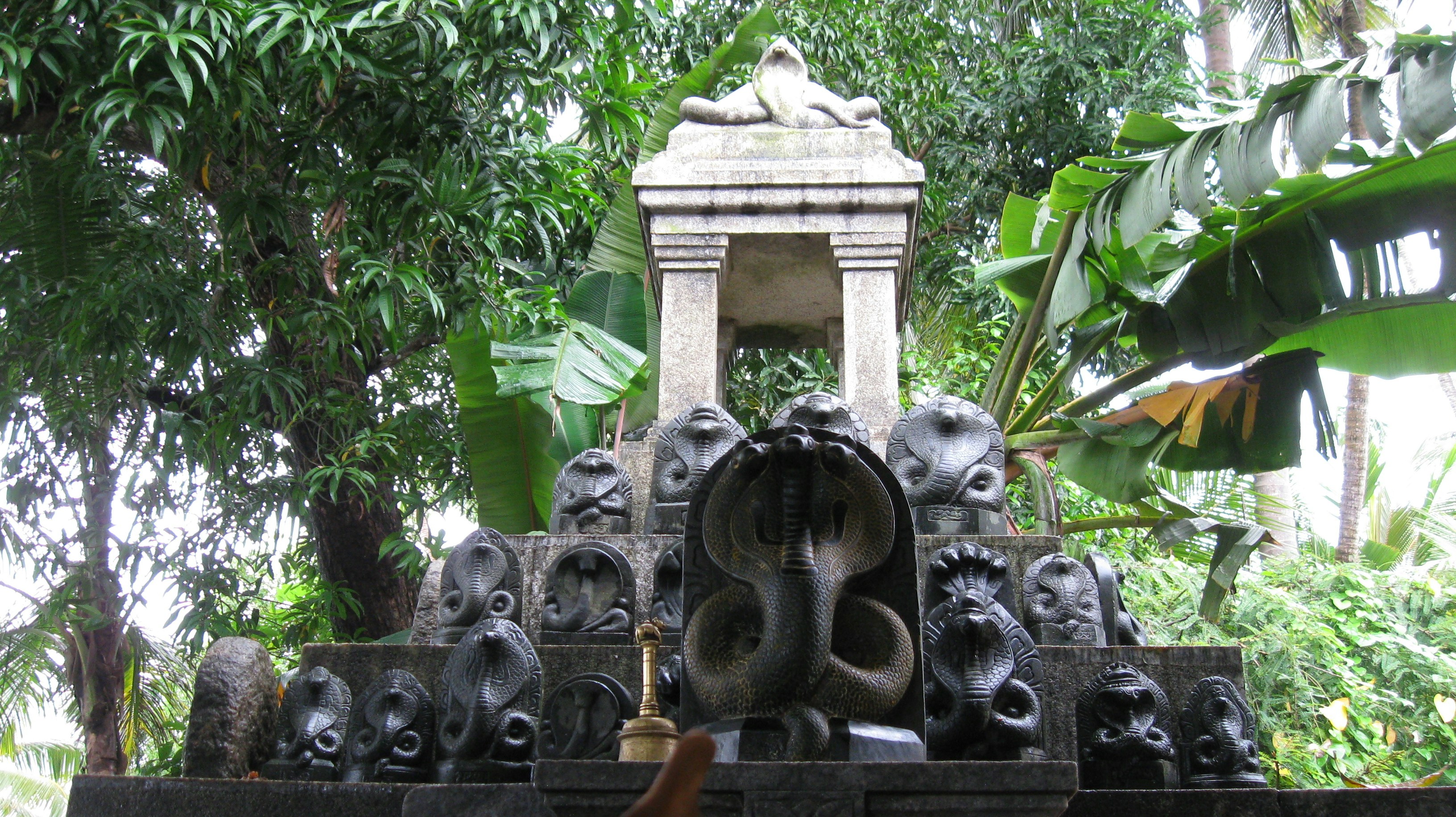 Stone carvings of serpent deities in a lush, green setting with a central shrine.