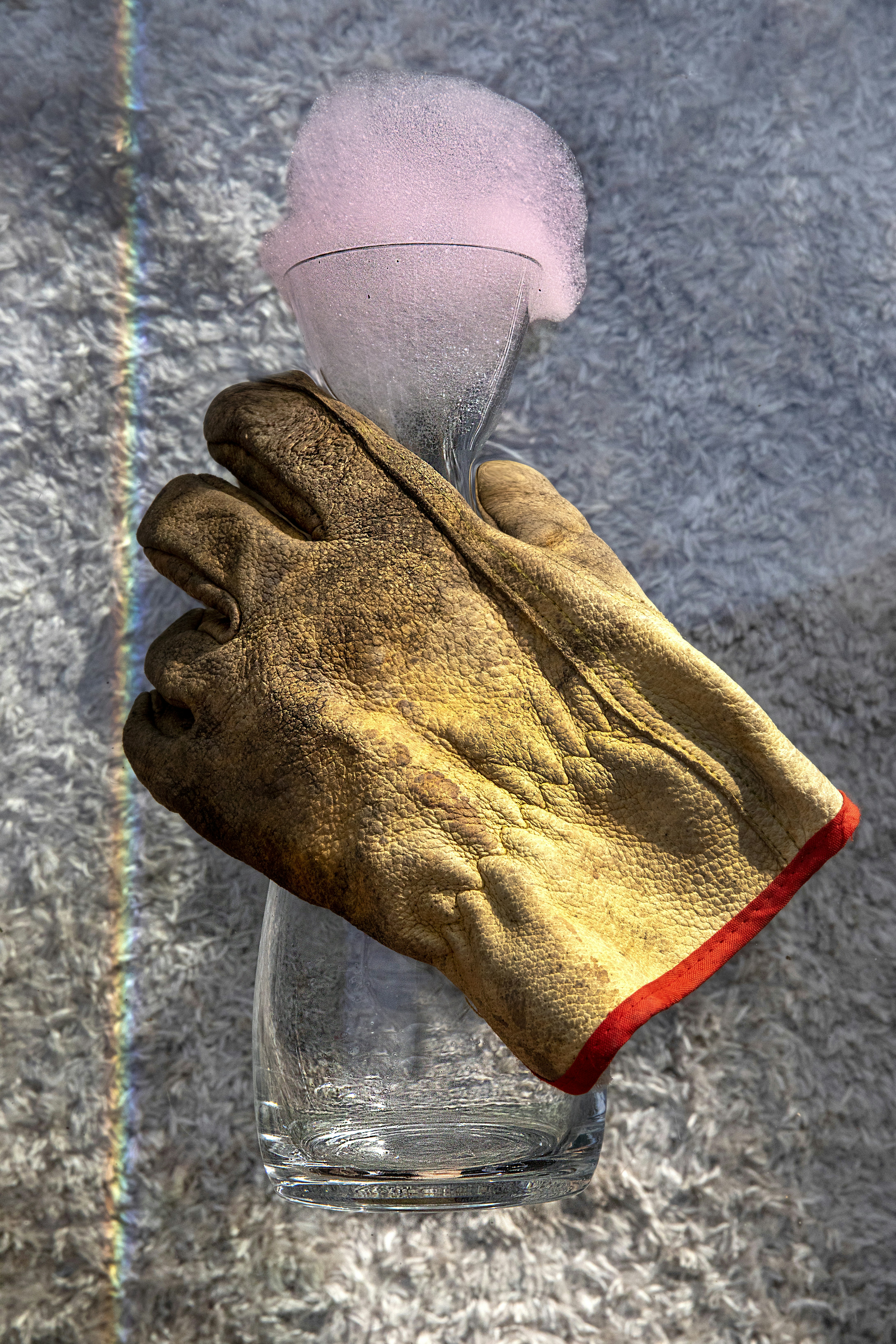 Grip and Glow: A Leather Glove Clutches a Pink-Top Glass Against a Textured Grey Backdrop