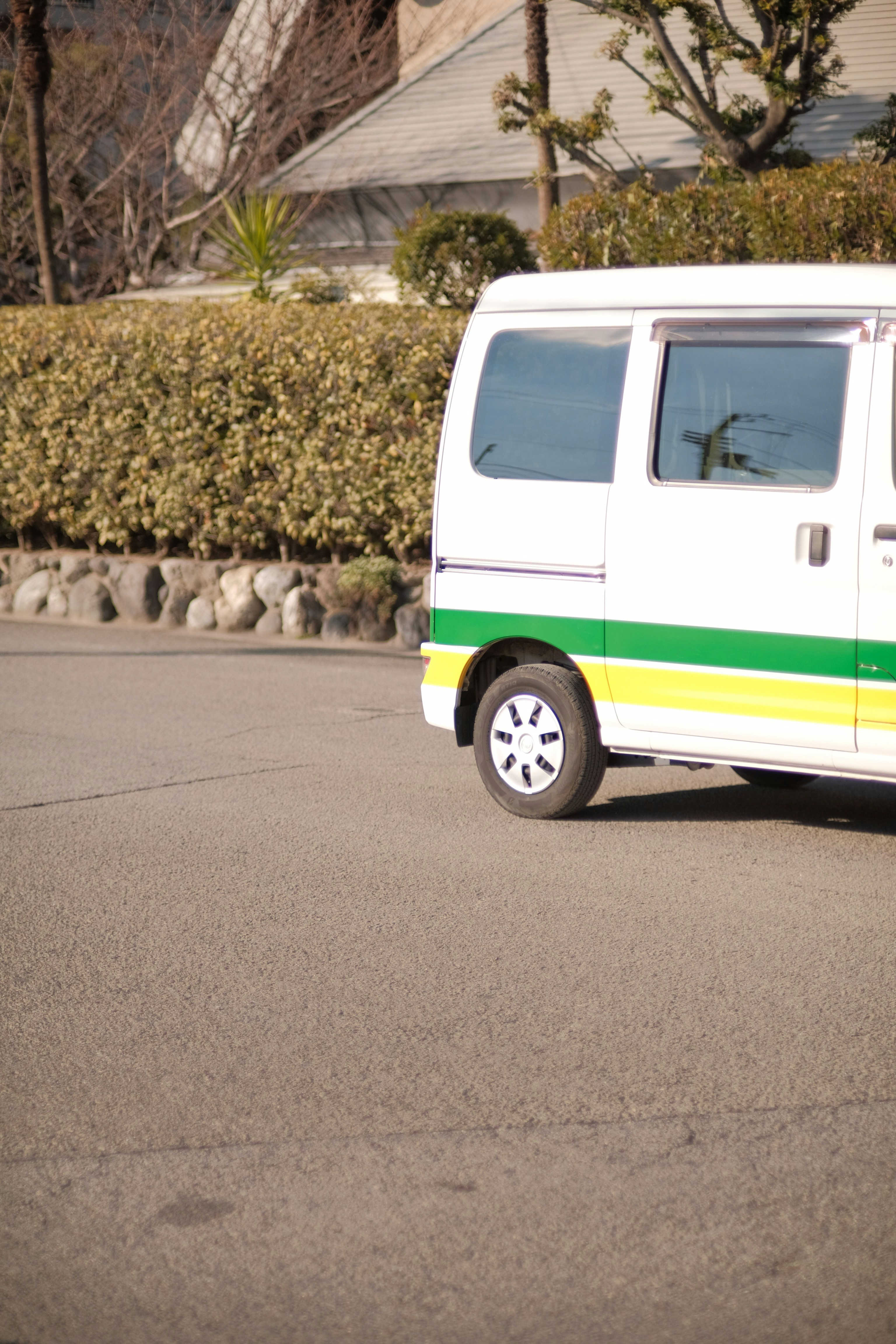 White utility van with green and yellow stripe parked on a sunlit street