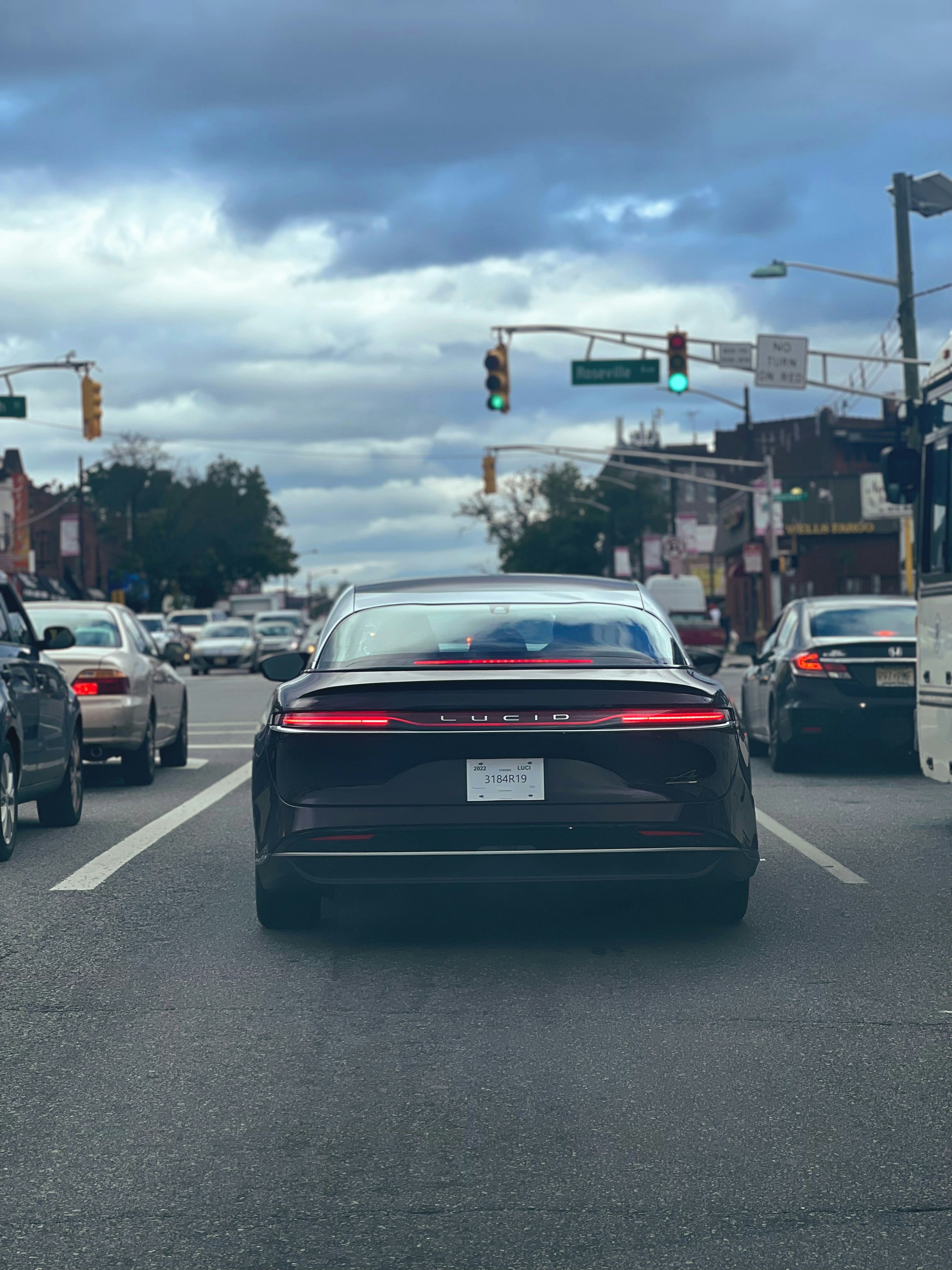 Sleek car waiting at a traffic light under a cloudy sky in an urban setting.