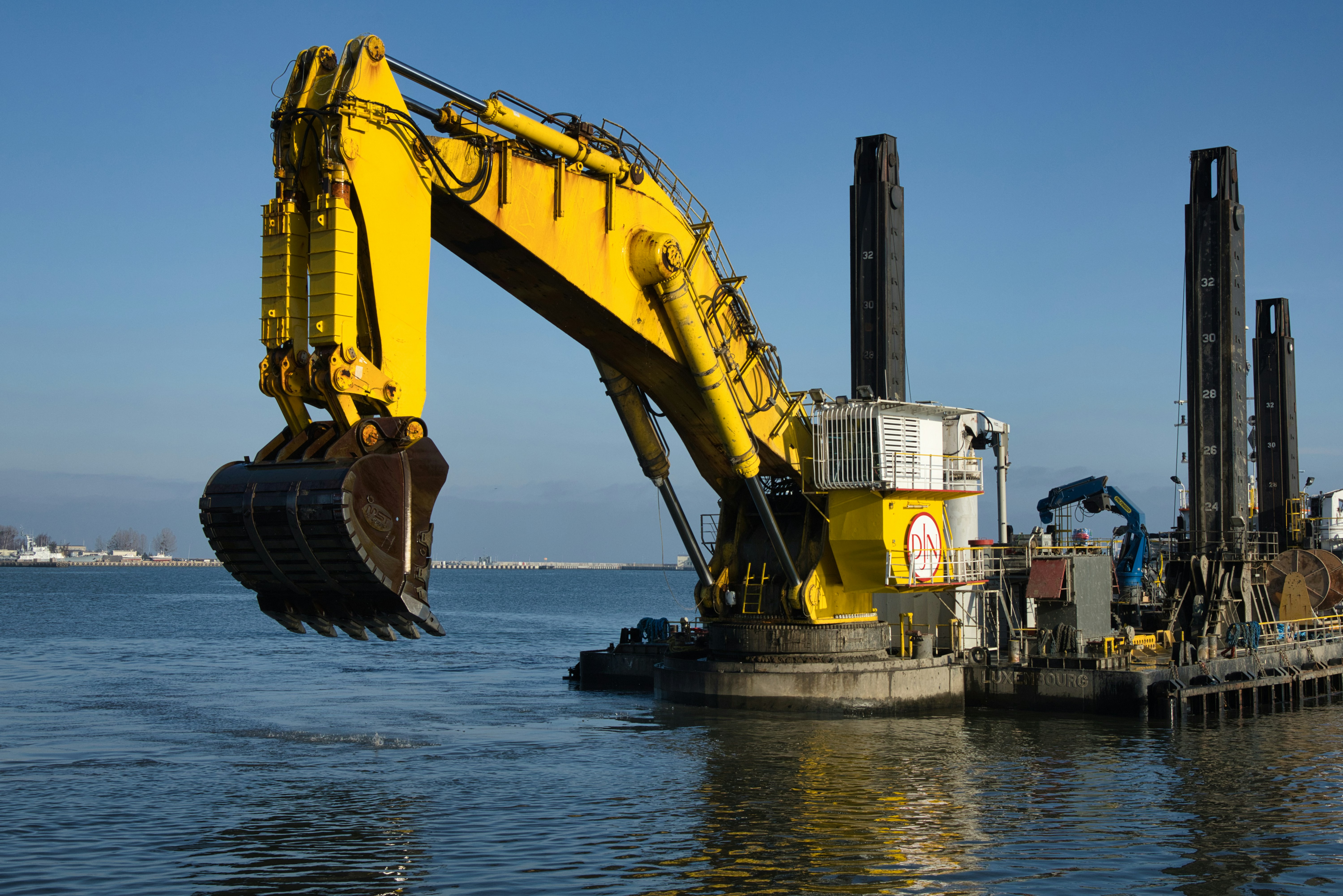 A large yellow excavator sitting on top of a body of water photo – Free ...