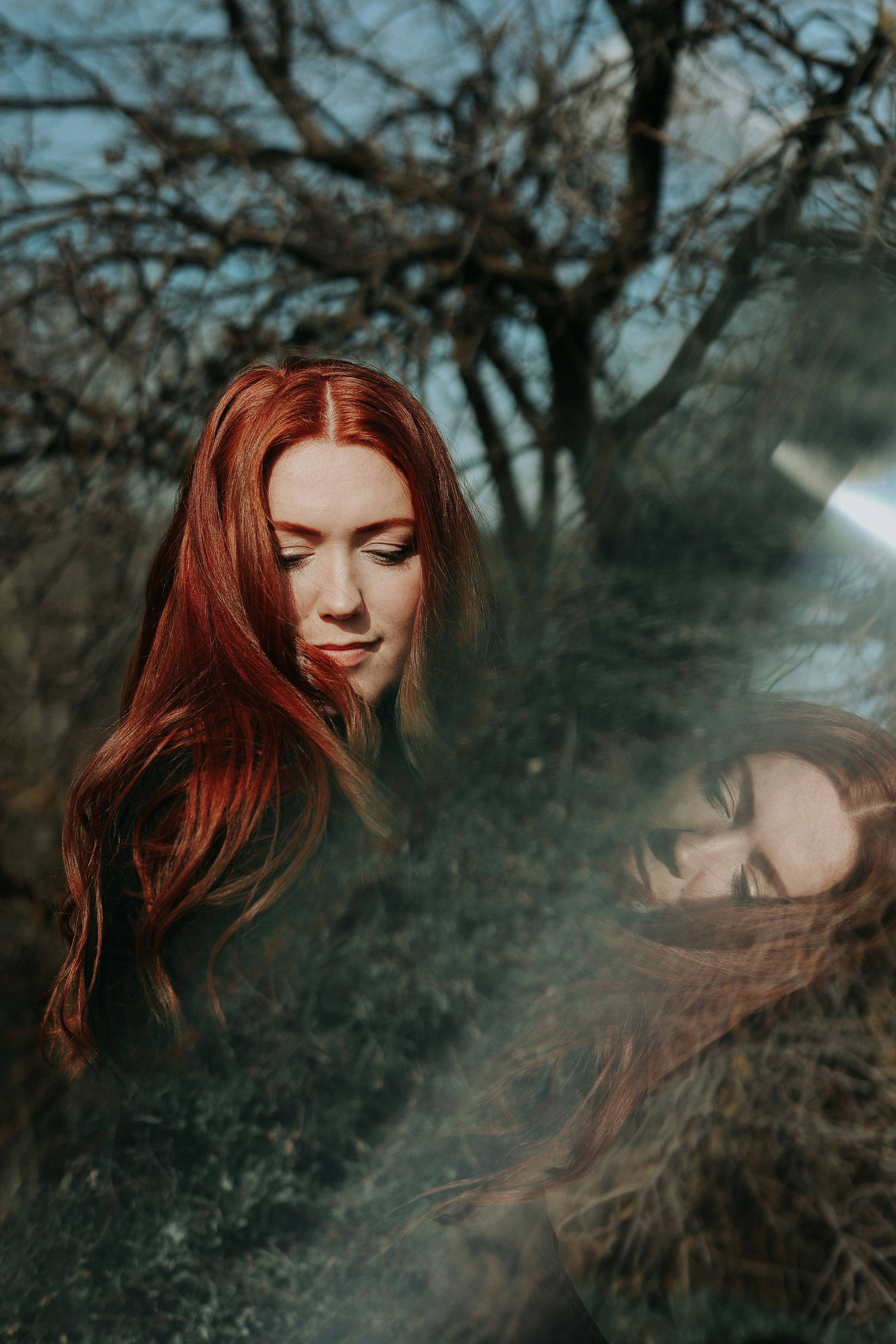 a woman with red hair standing next to a tree