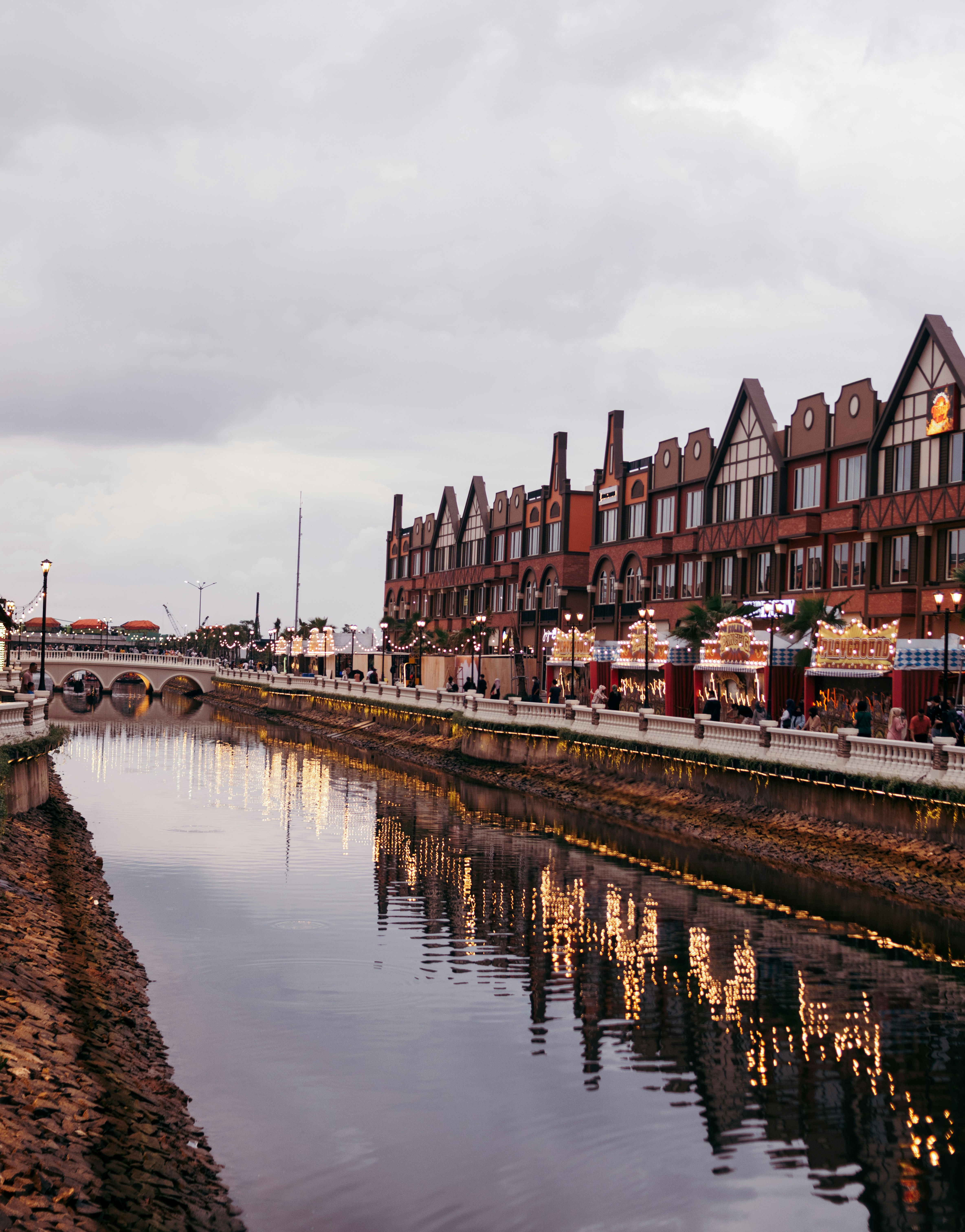 Row of charming brick buildings mirrored in a tranquil canal under a cloudy sky.