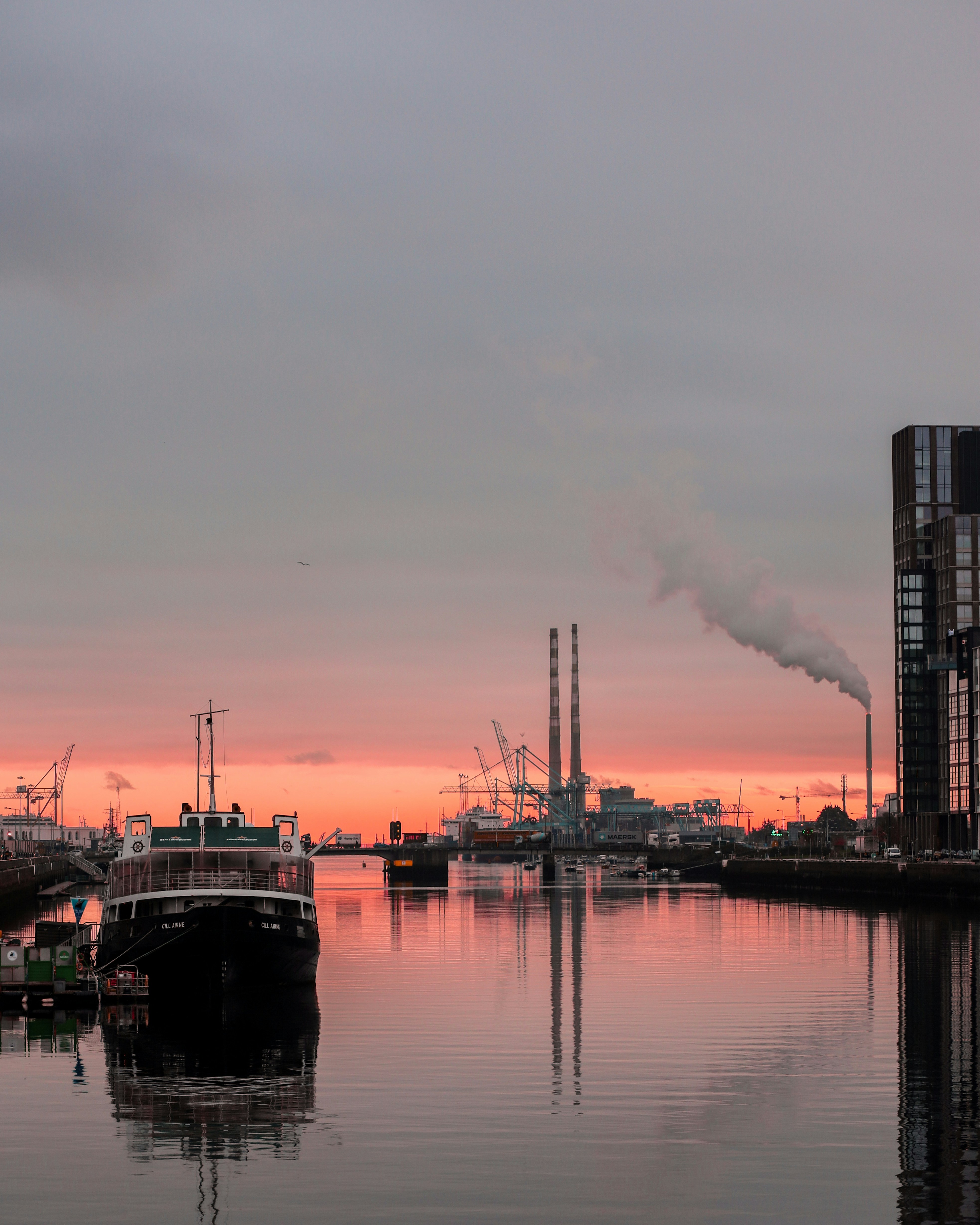 Industrial glow at dusk: ships and smoke rising over a calm harbor