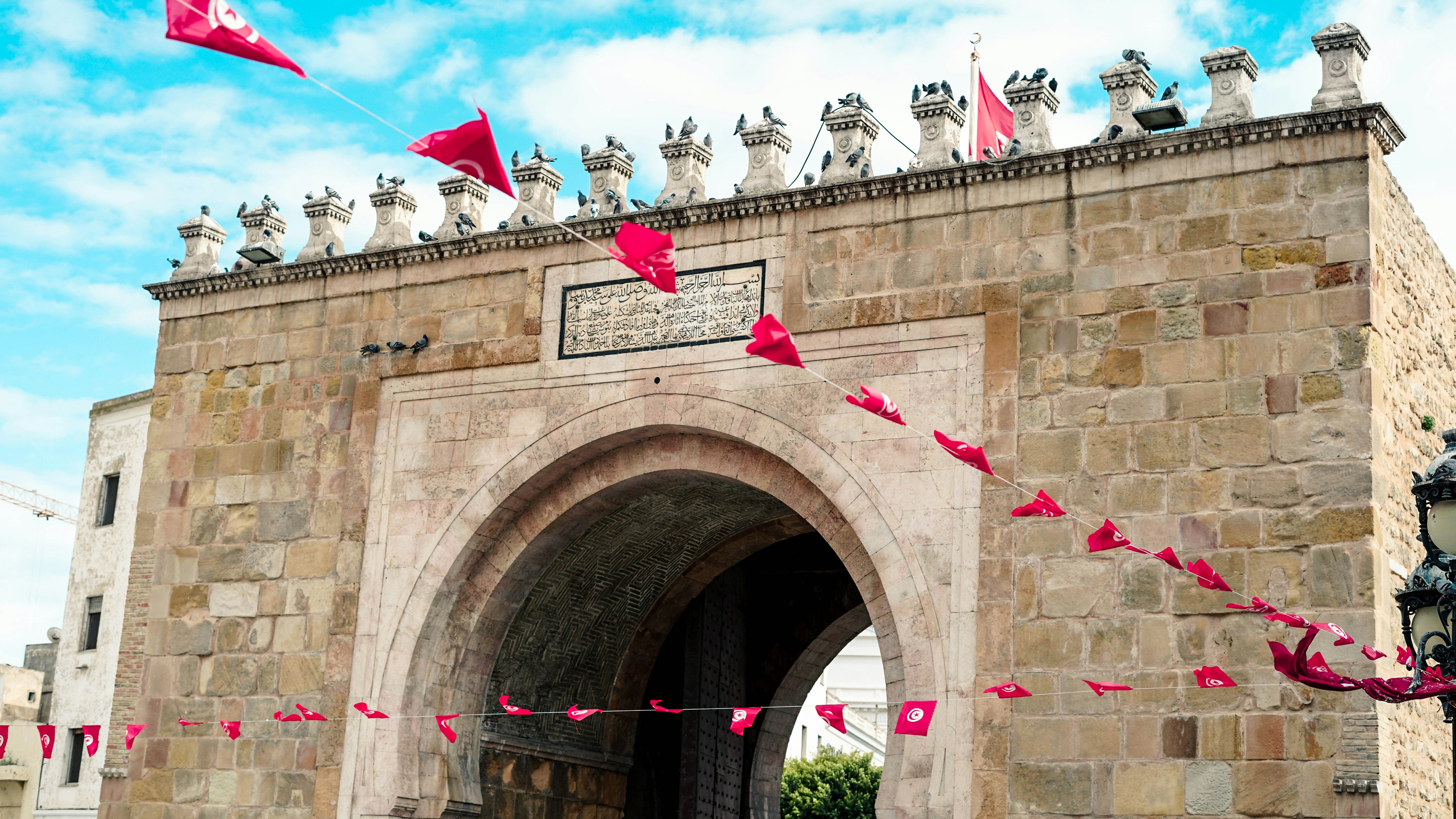 Stone archway decorated with red flags under a bright blue sky.