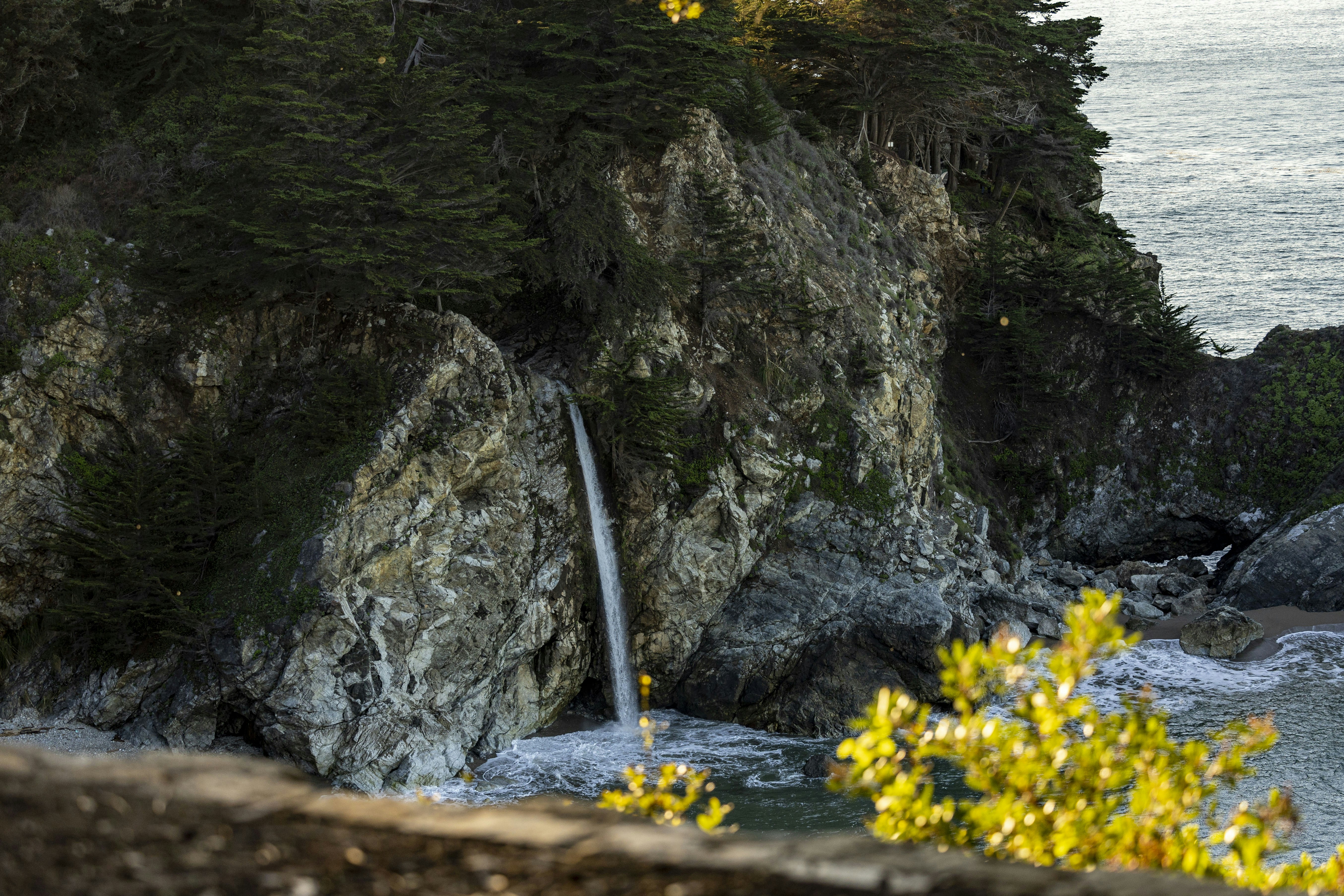A waterfall is coming out of a cliff into the ocean photo – Free Coast ...