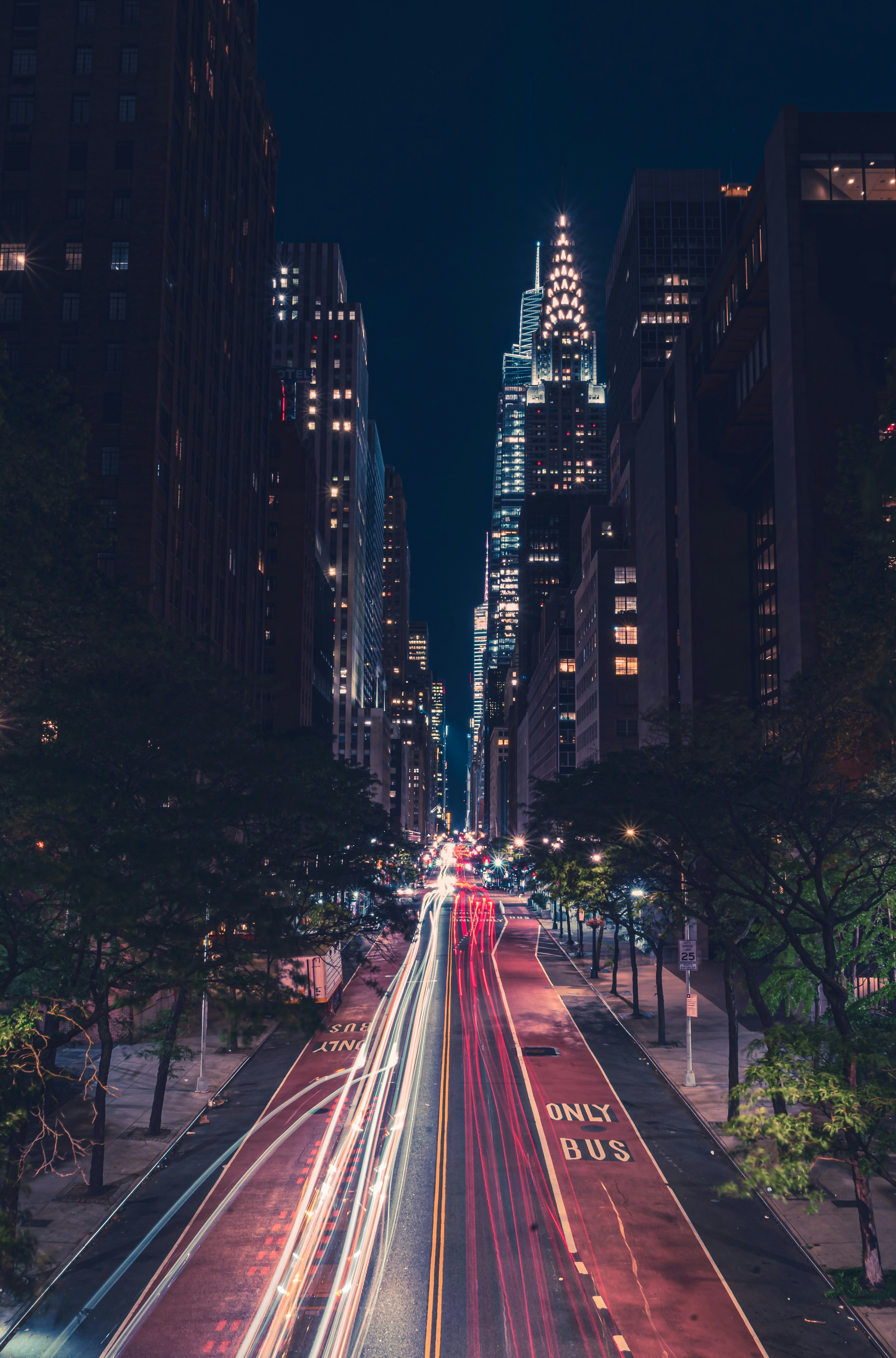 Long exposure of a bustling city street at night with light trails from moving traffic and illuminated skyscrapers.