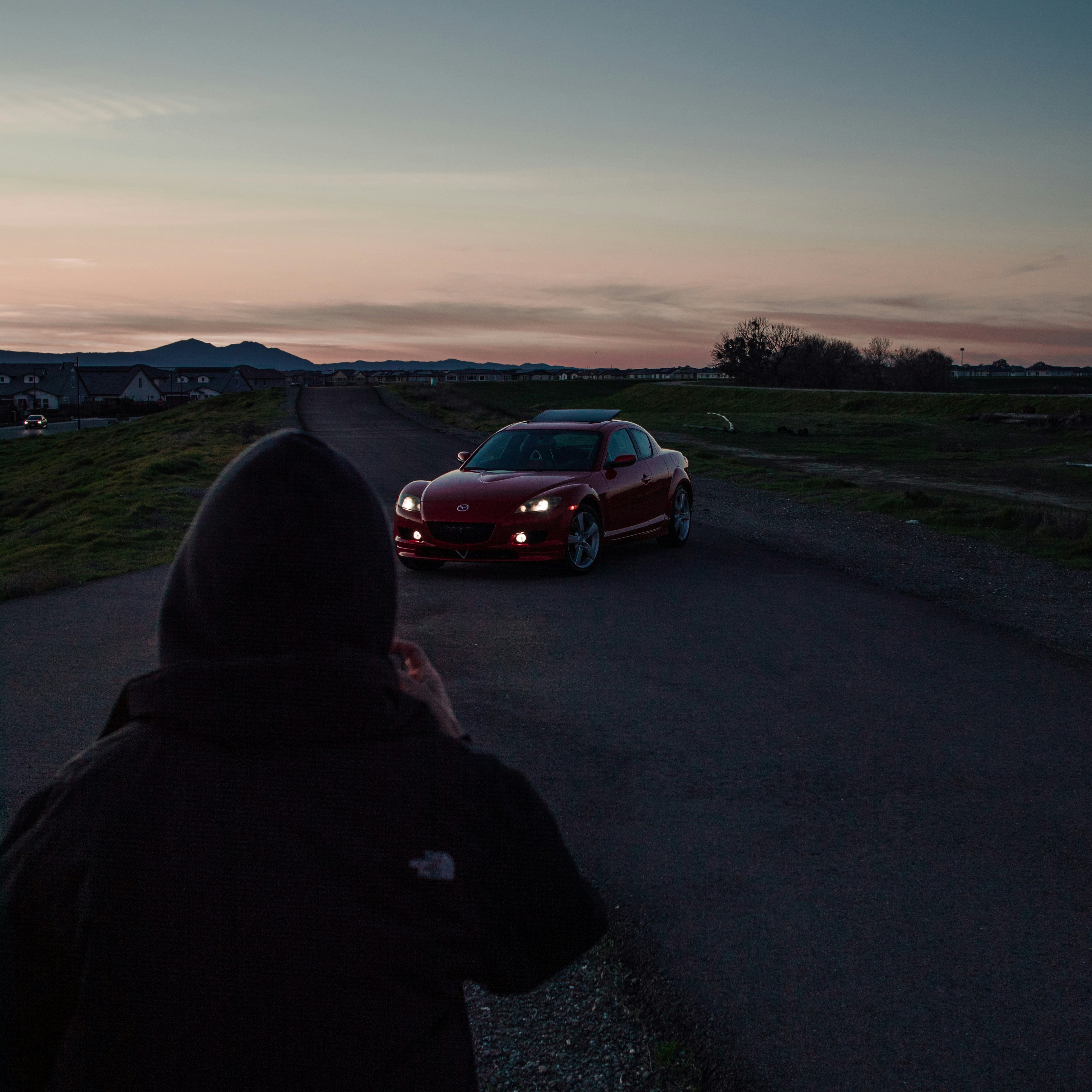 a person in a hoodie taking a picture of a car