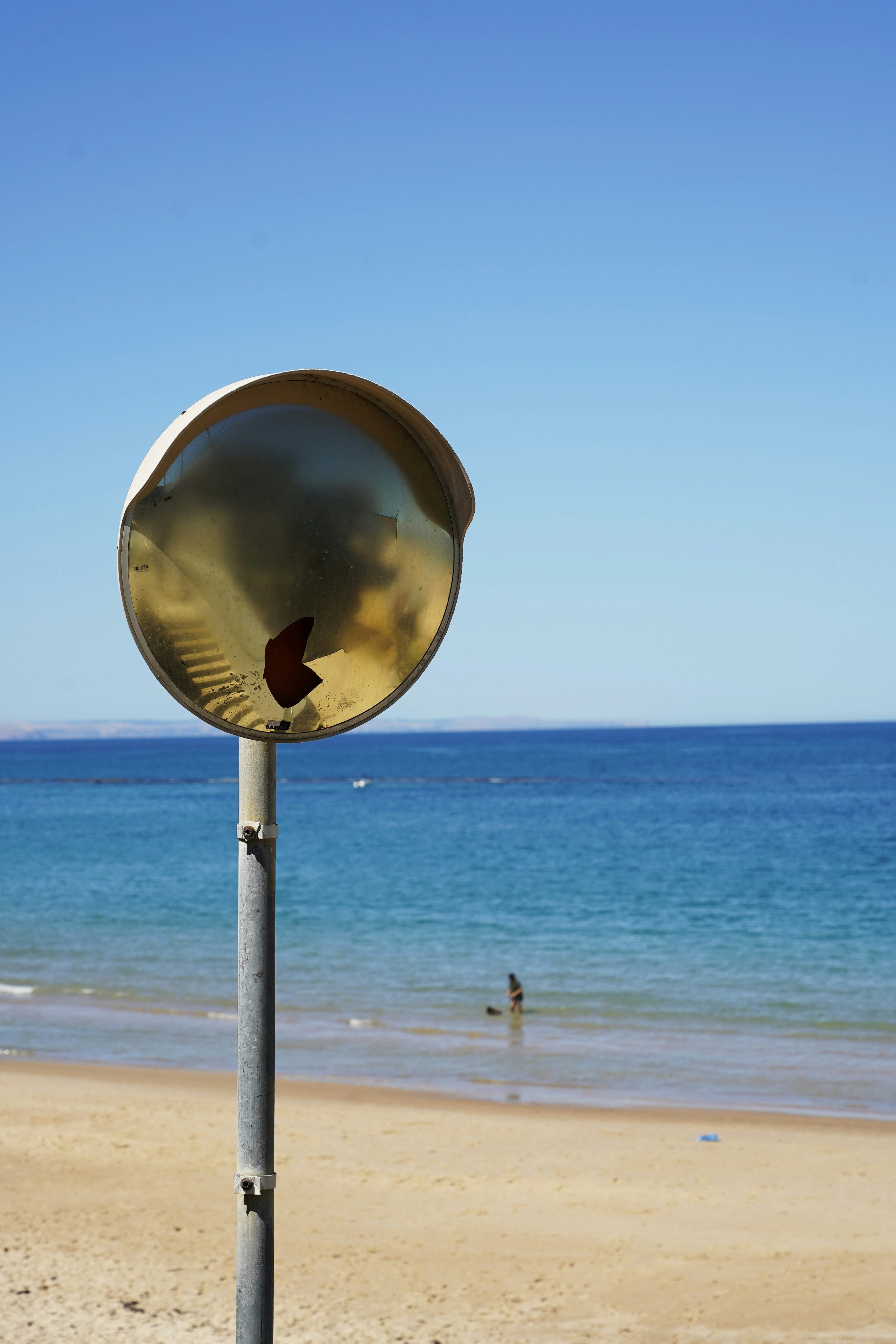 Coastal Sentinel: Weathered Circular Mirror Framing a Quiet Beach