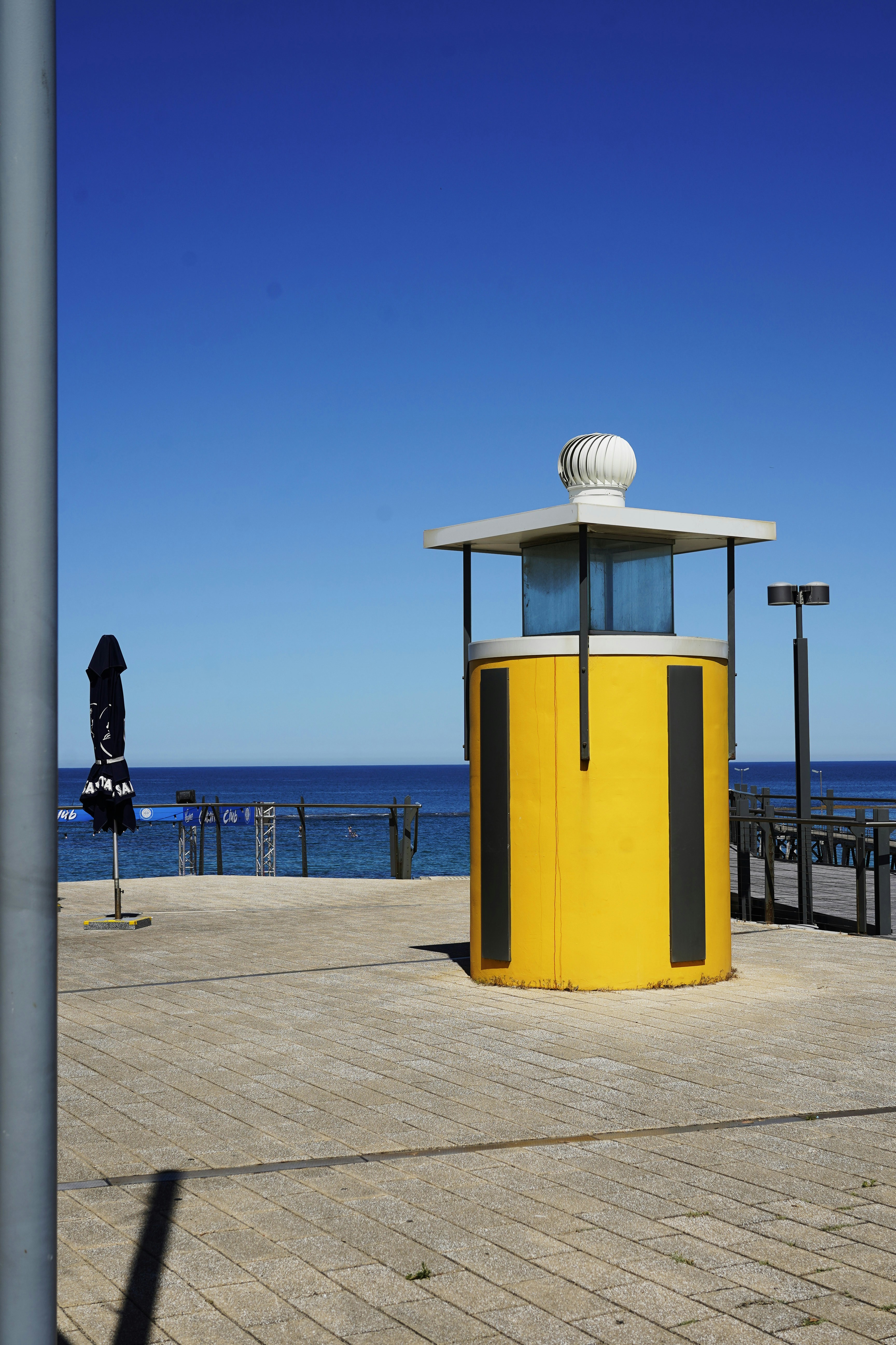 Yellow Sentinel by the Sea: A Pier’s Bright Cylinder in Blue Light