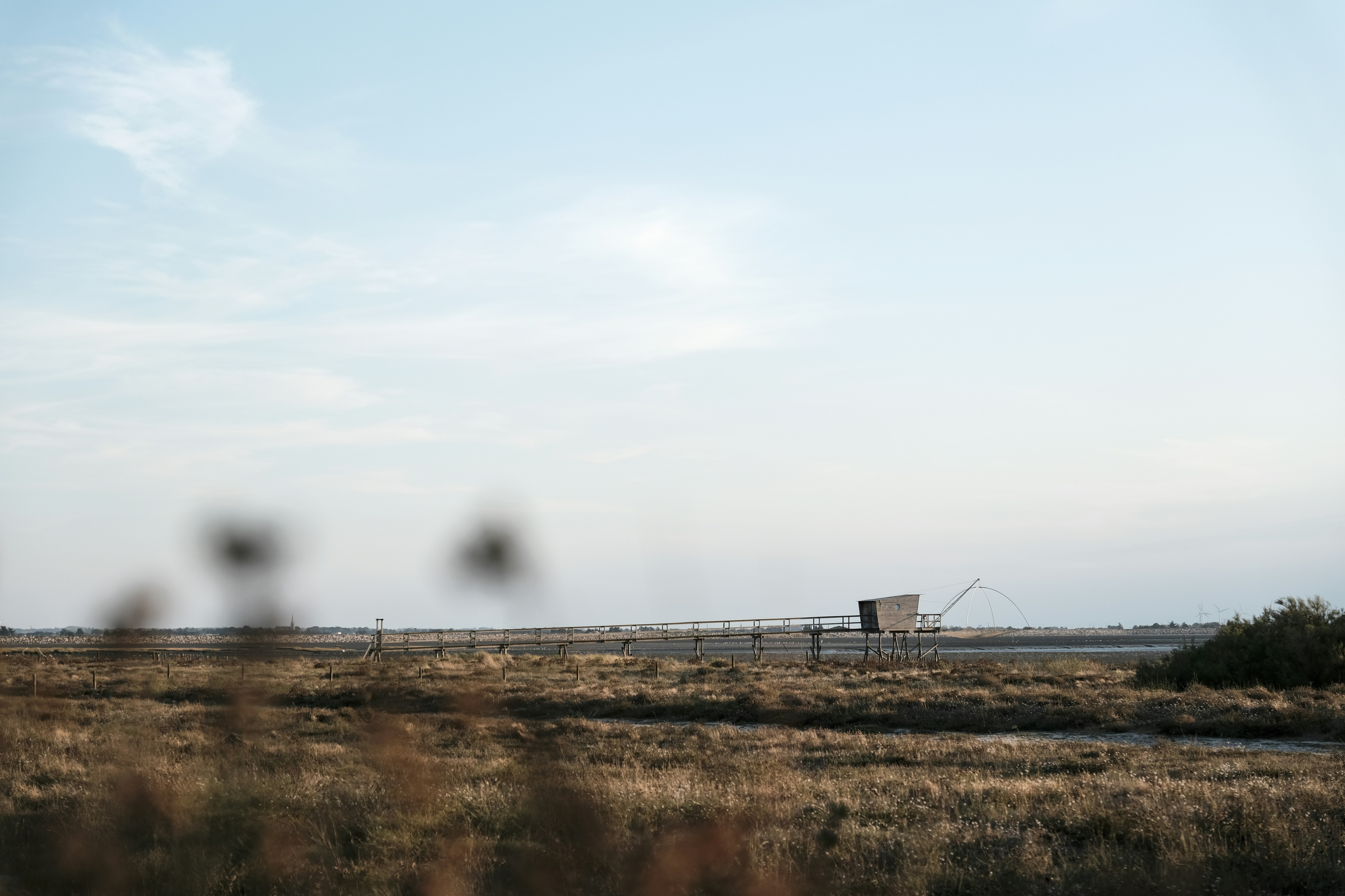 Distant structure on a vast, dry grassland under a clear blue sky.