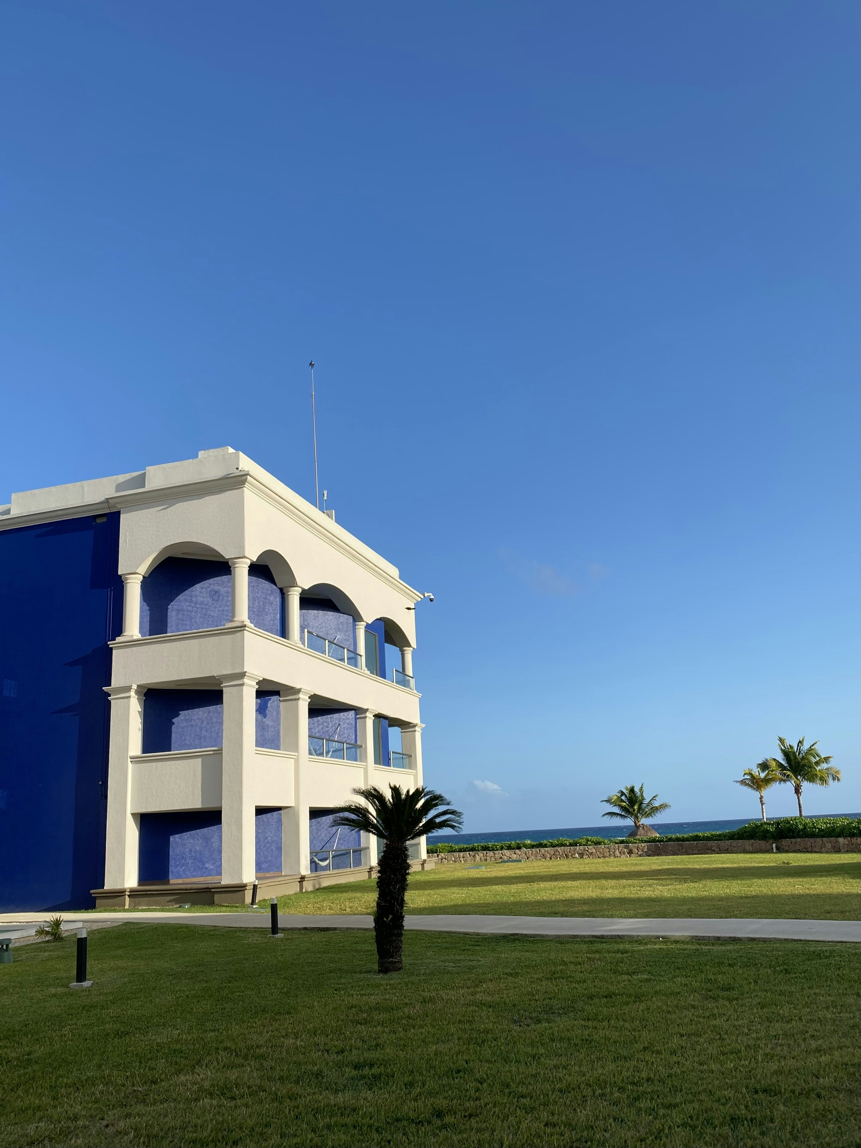 Modern coastal building with vibrant blue accents, set against a clear sky and palm trees. The scene evokes a sense of tranquility and leisure.
