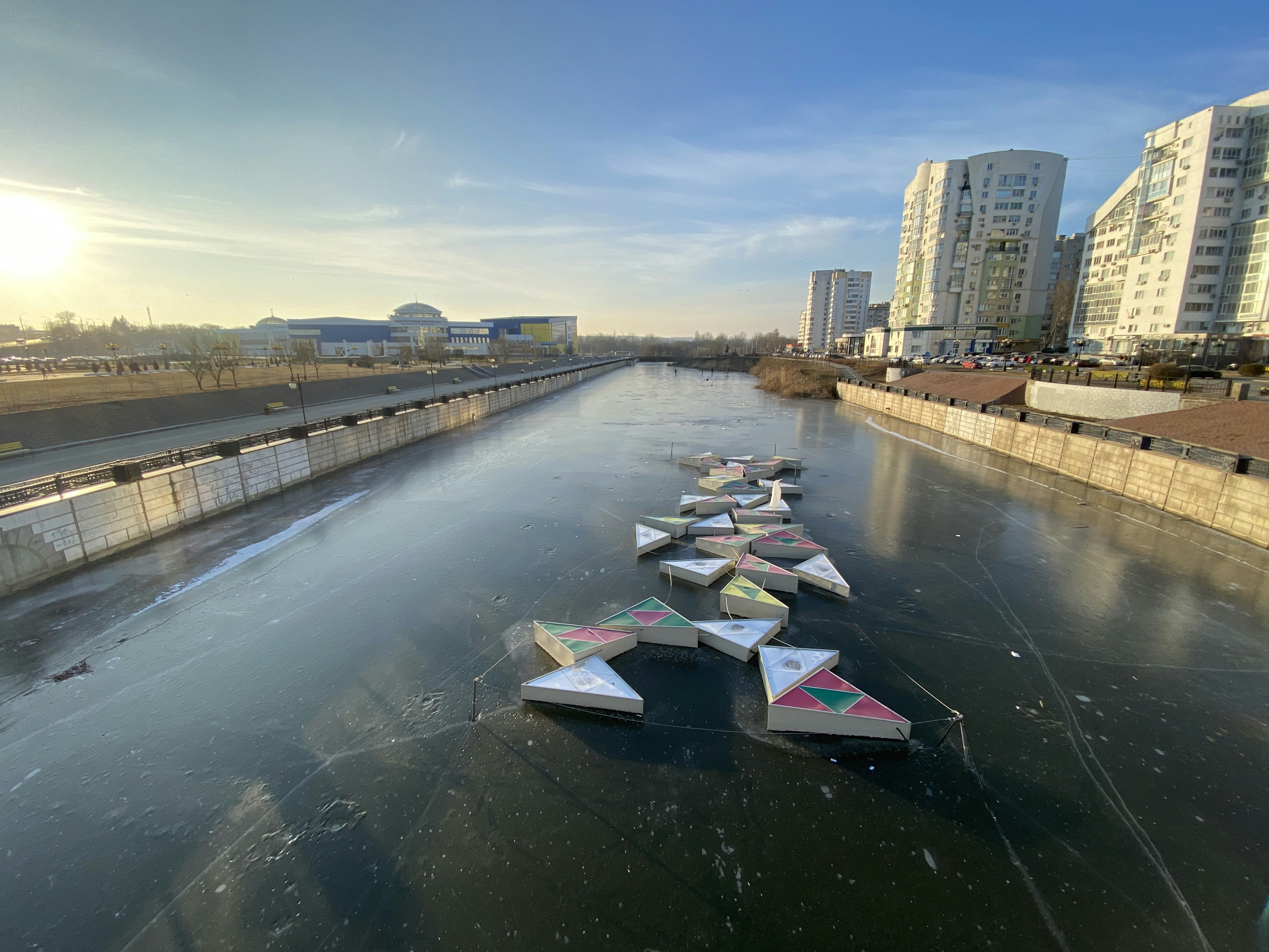 Prismatic Pyramids Drift on a Frozen Canal by the City Skyline at Sunset