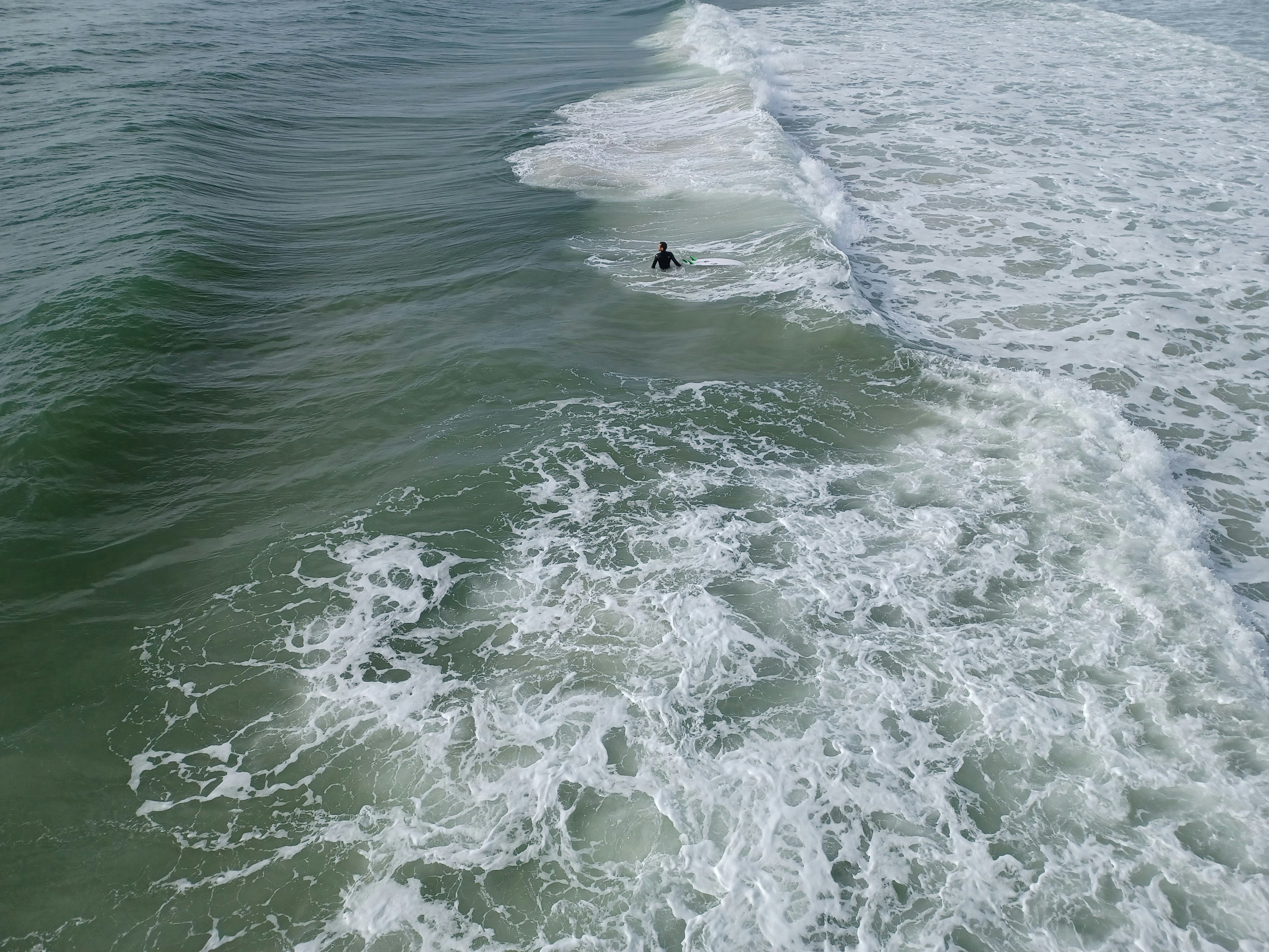 A lone surfer navigating the rolling waves under a clear sky, capturing the essence of adventure and tranquility. The scene highlights the dynamic interplay between water and surf.