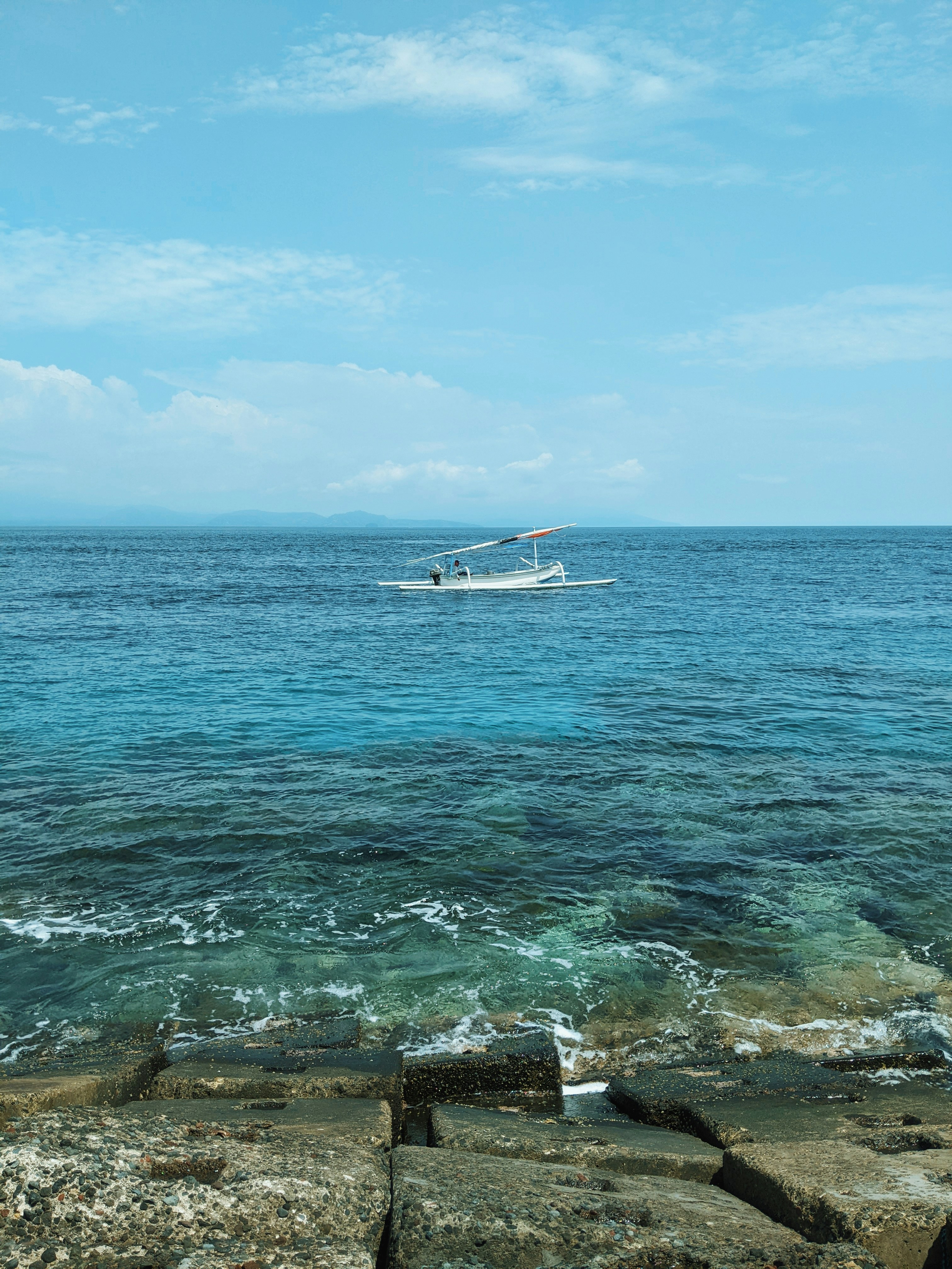 A traditional boat glides across clear blue waters, framed by rocky shorelines and a distant horizon under a bright sky.