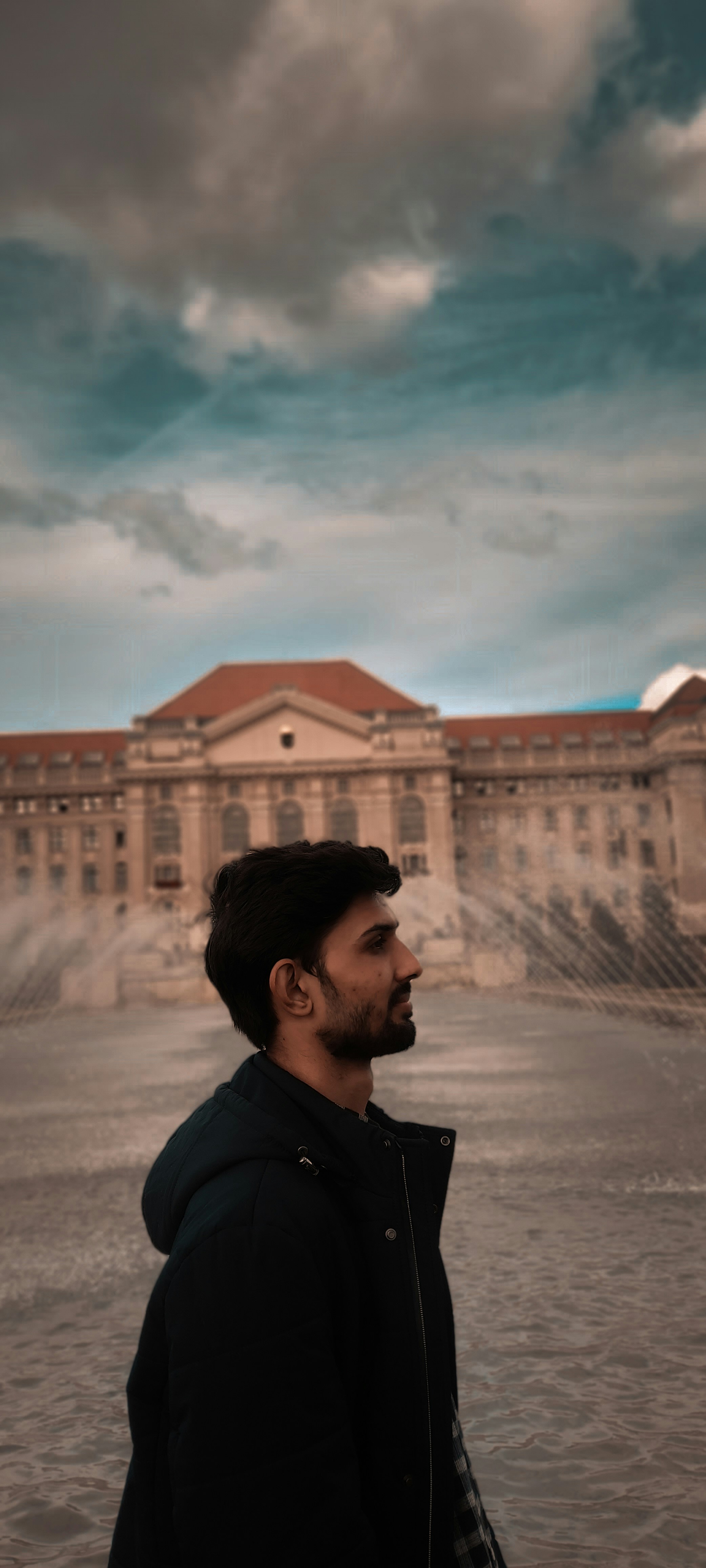 A profile of a man standing against a majestic historic building, with a dramatic sky overhead. The scene conveys a sense of calm and contemplation.