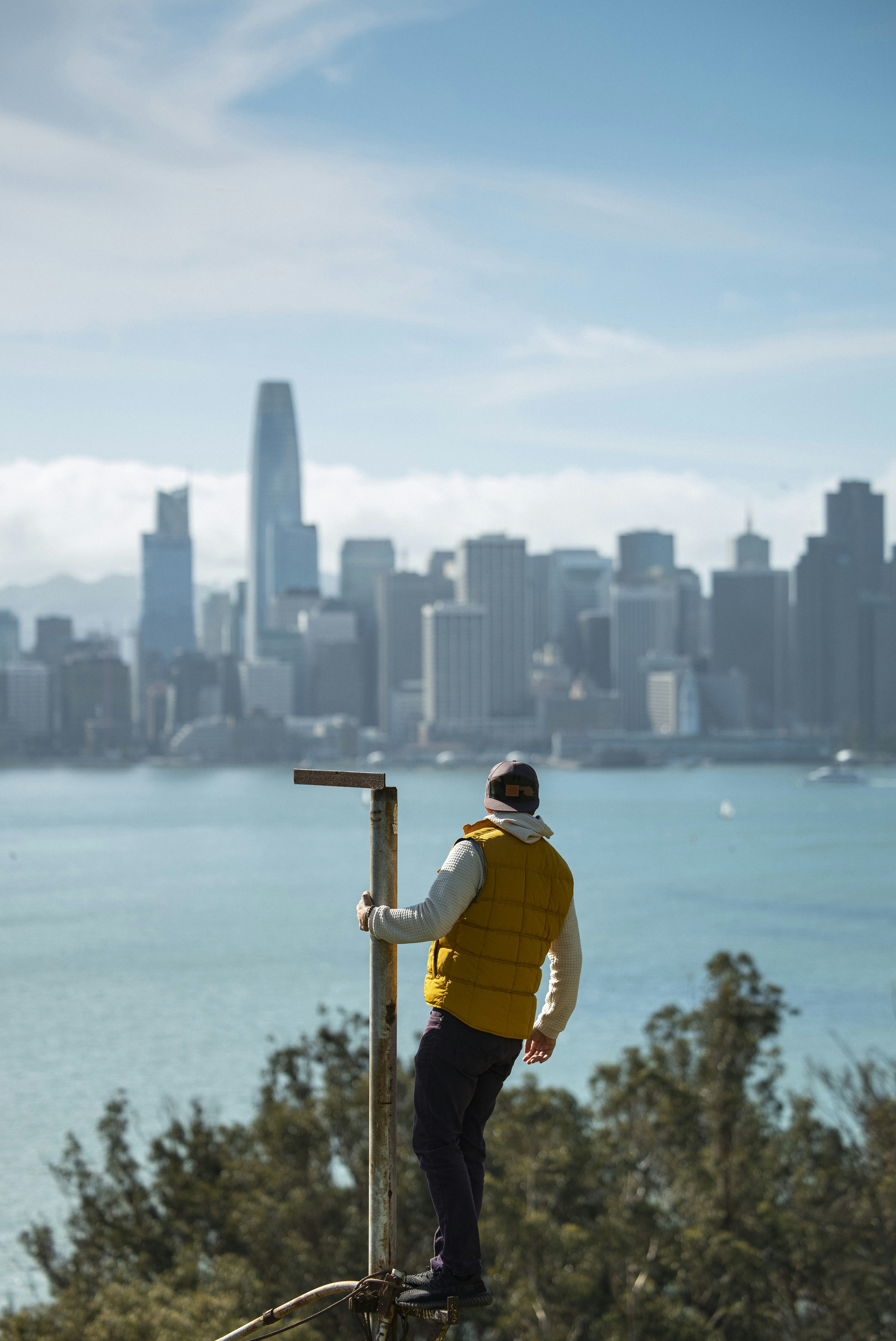 A person in a yellow vest gazes over a city skyline from a vantage point, capturing the blend of nature and urban life. The scene conveys a sense of exploration and tranquility.