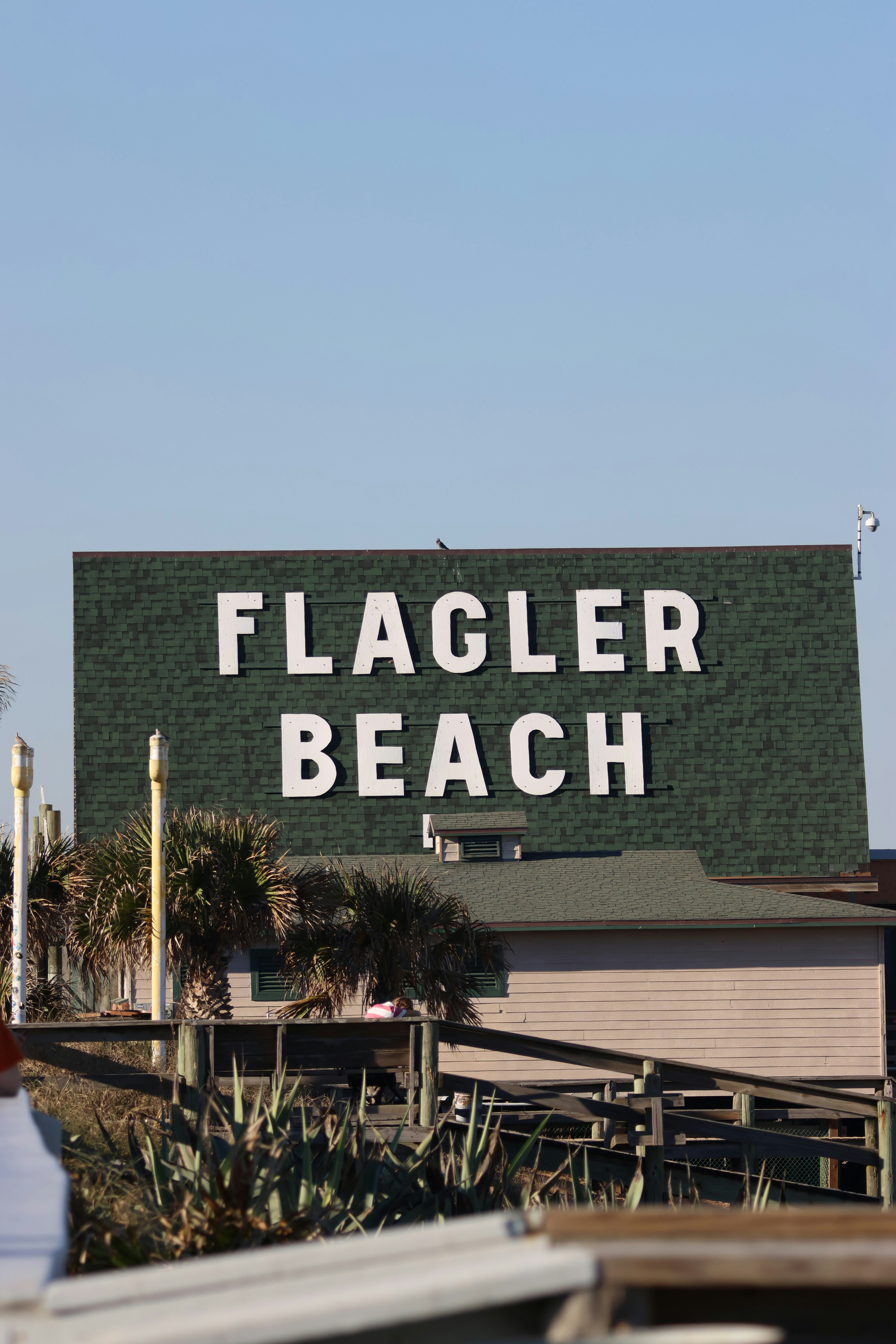 Flagler Beach Signboard: Green Tile Landmark Framed by Palms and Docks
