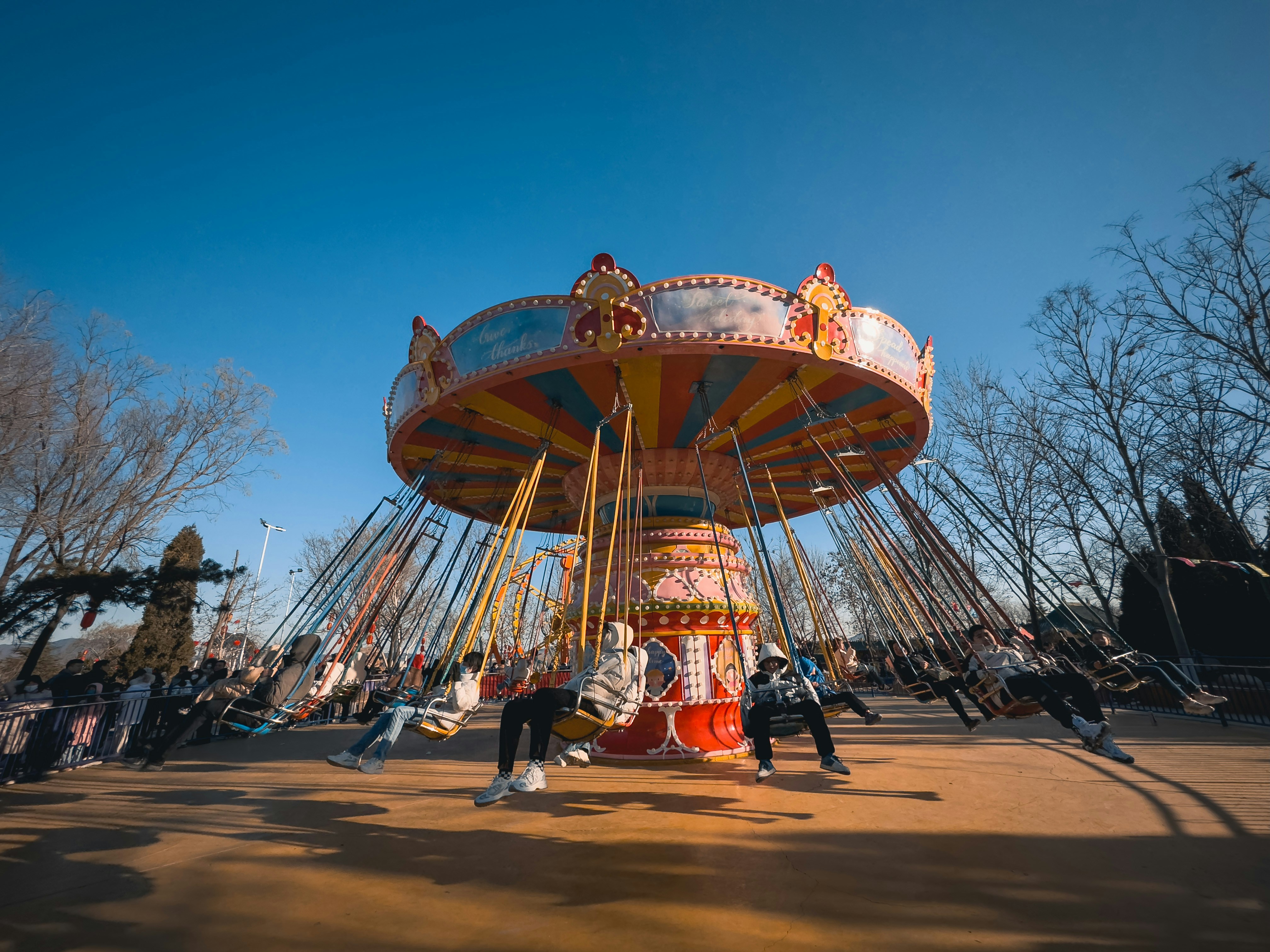 Carousel swings spinning against a clear blue sky, surrounded by leafless trees.