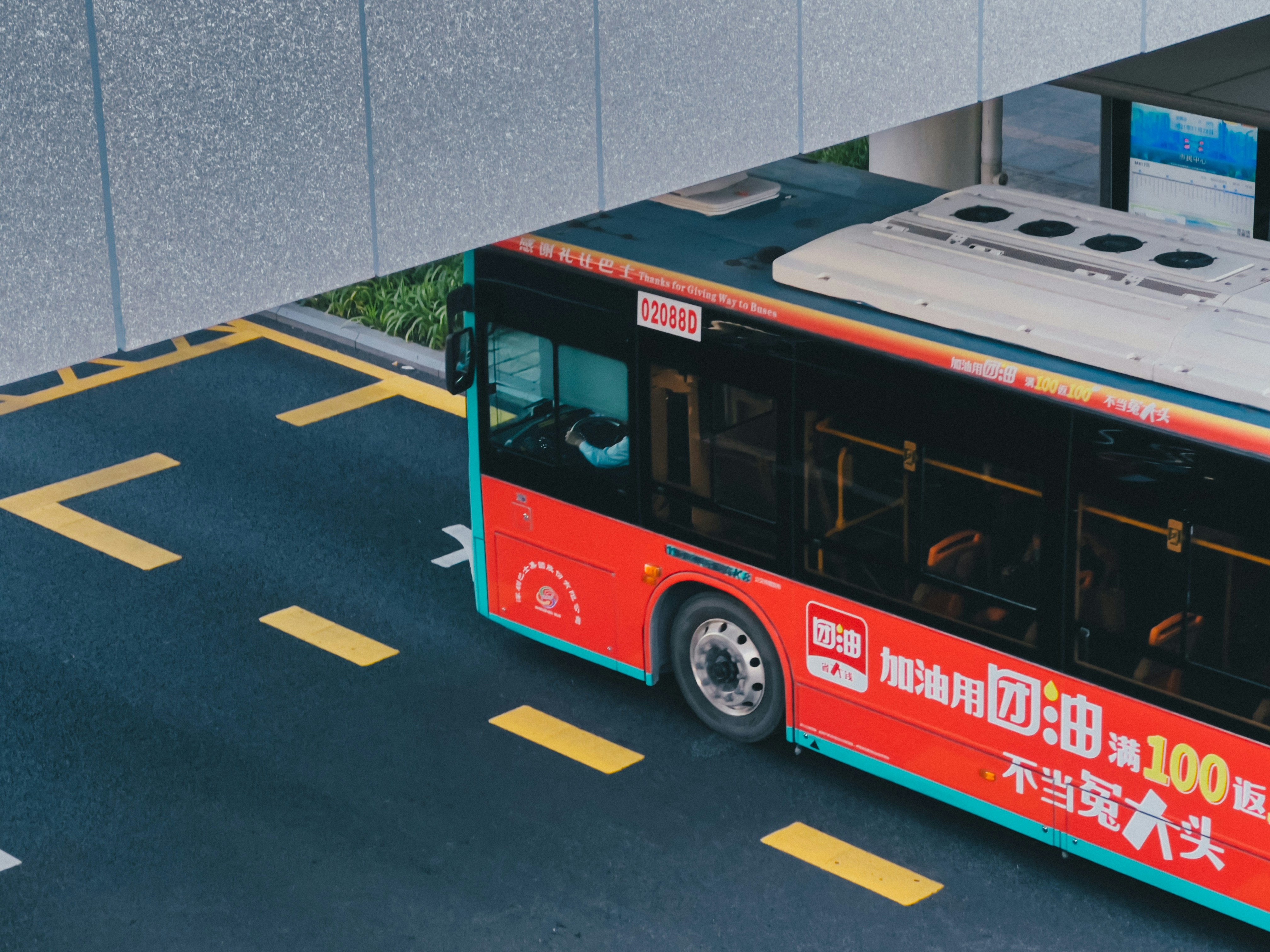 A red bus driving down a street next to a tall building photo – Free ...