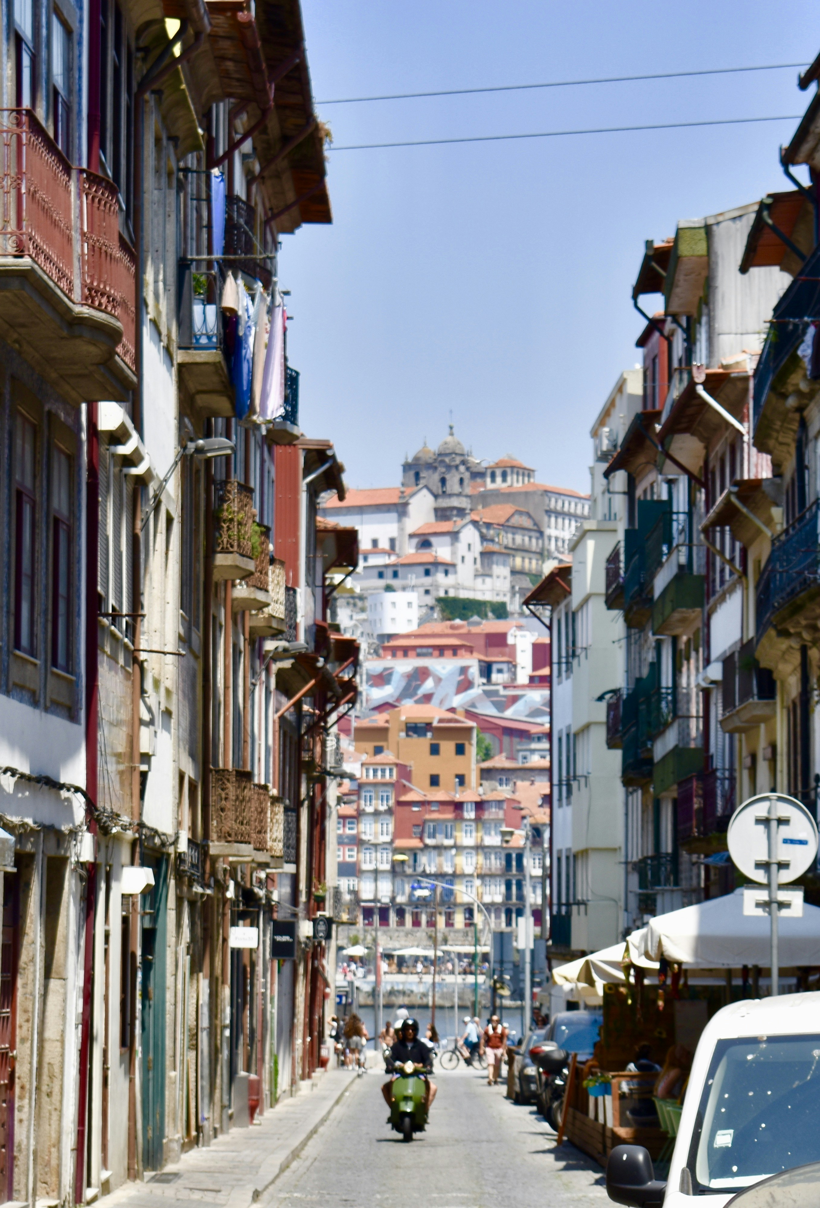 Narrow street lined with vibrant buildings leading to a picturesque hillside, where colorful houses rise against a clear blue sky.