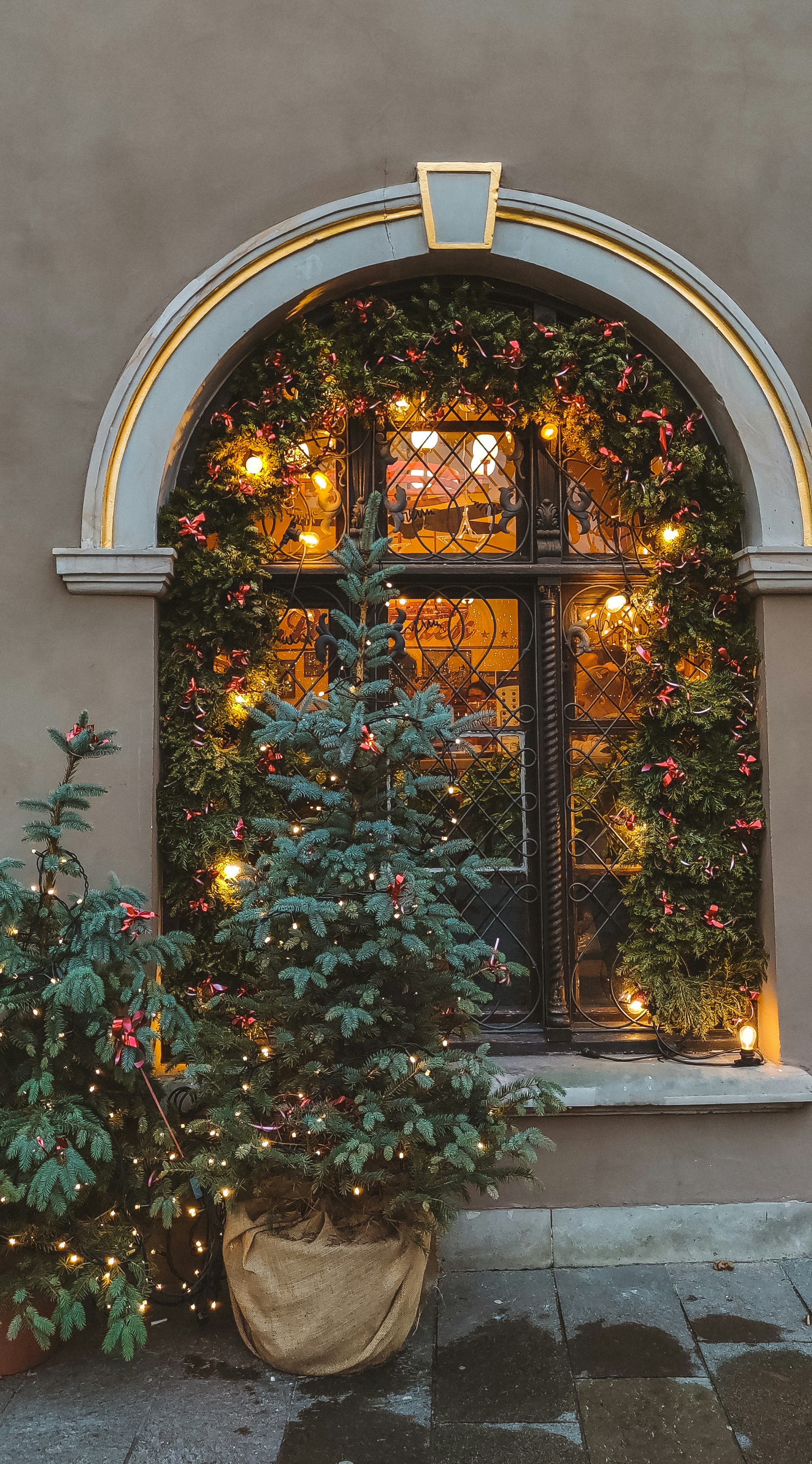 A beautifully adorned window framed by lush greenery and twinkling lights, evoking a cozy holiday spirit.