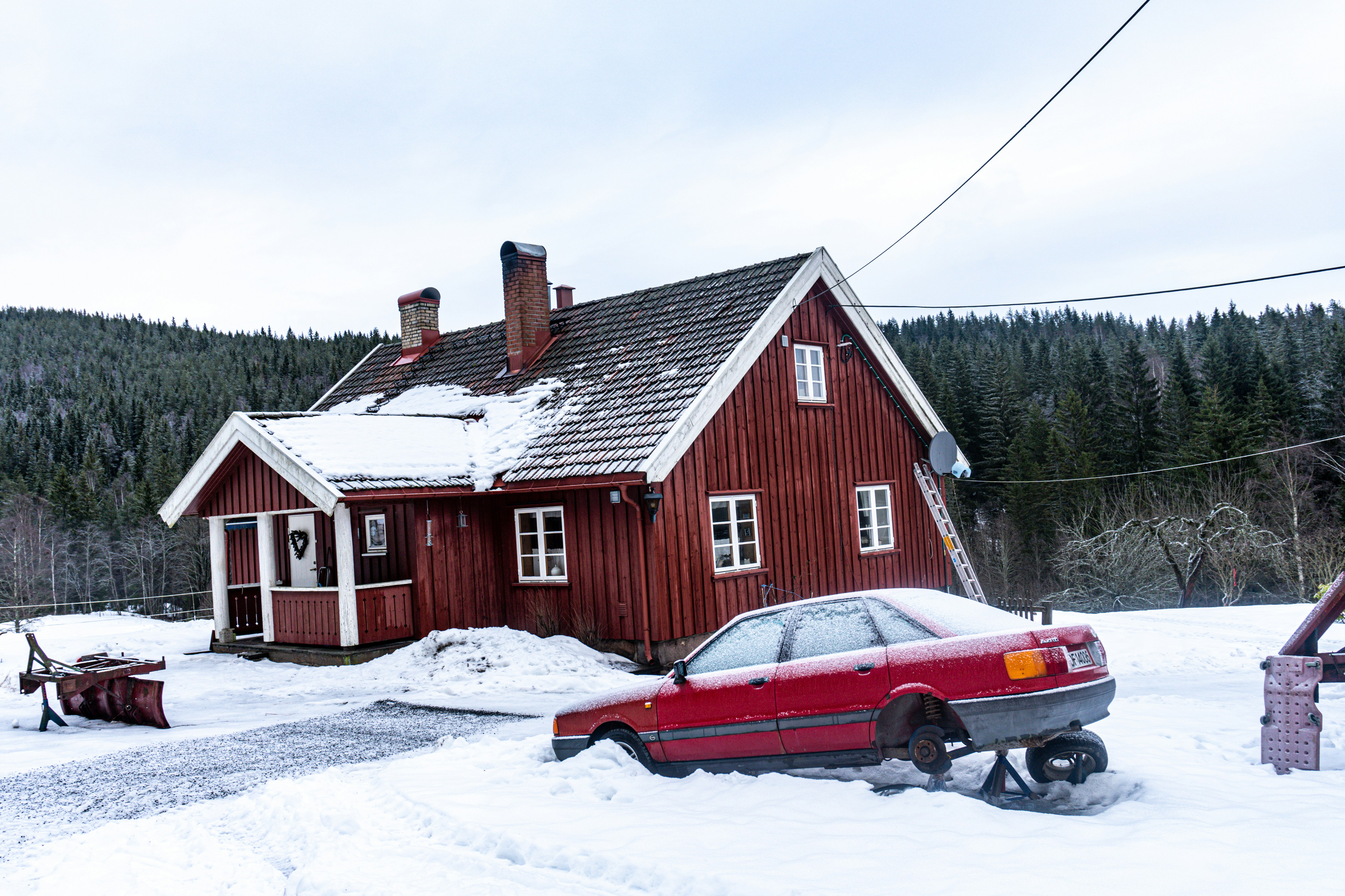 Snowbound Red Cabin Amid Pine Forest, with a Parked Car in Front