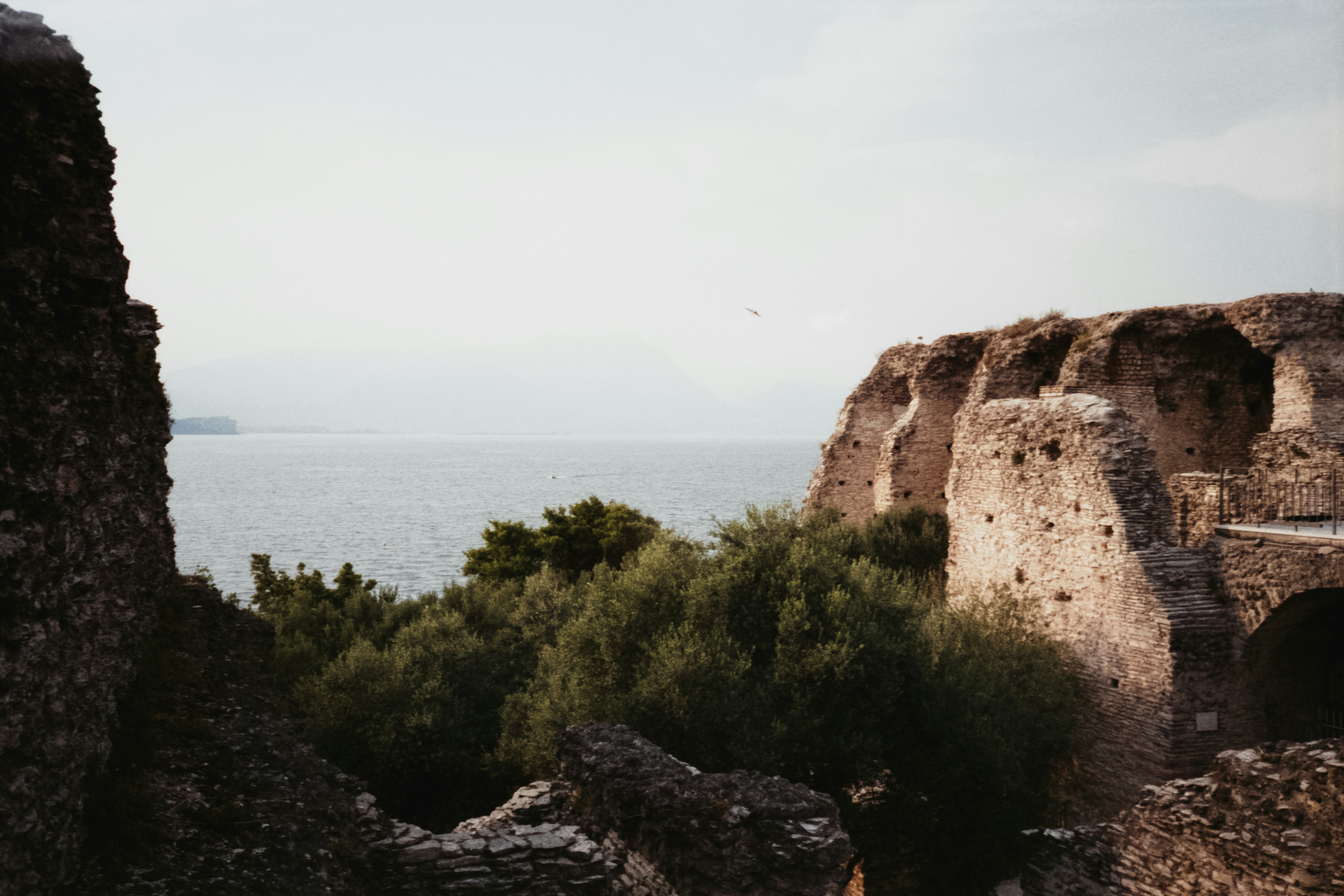 Rugged castle ruins frame a serene ocean view under a soft, overcast sky.