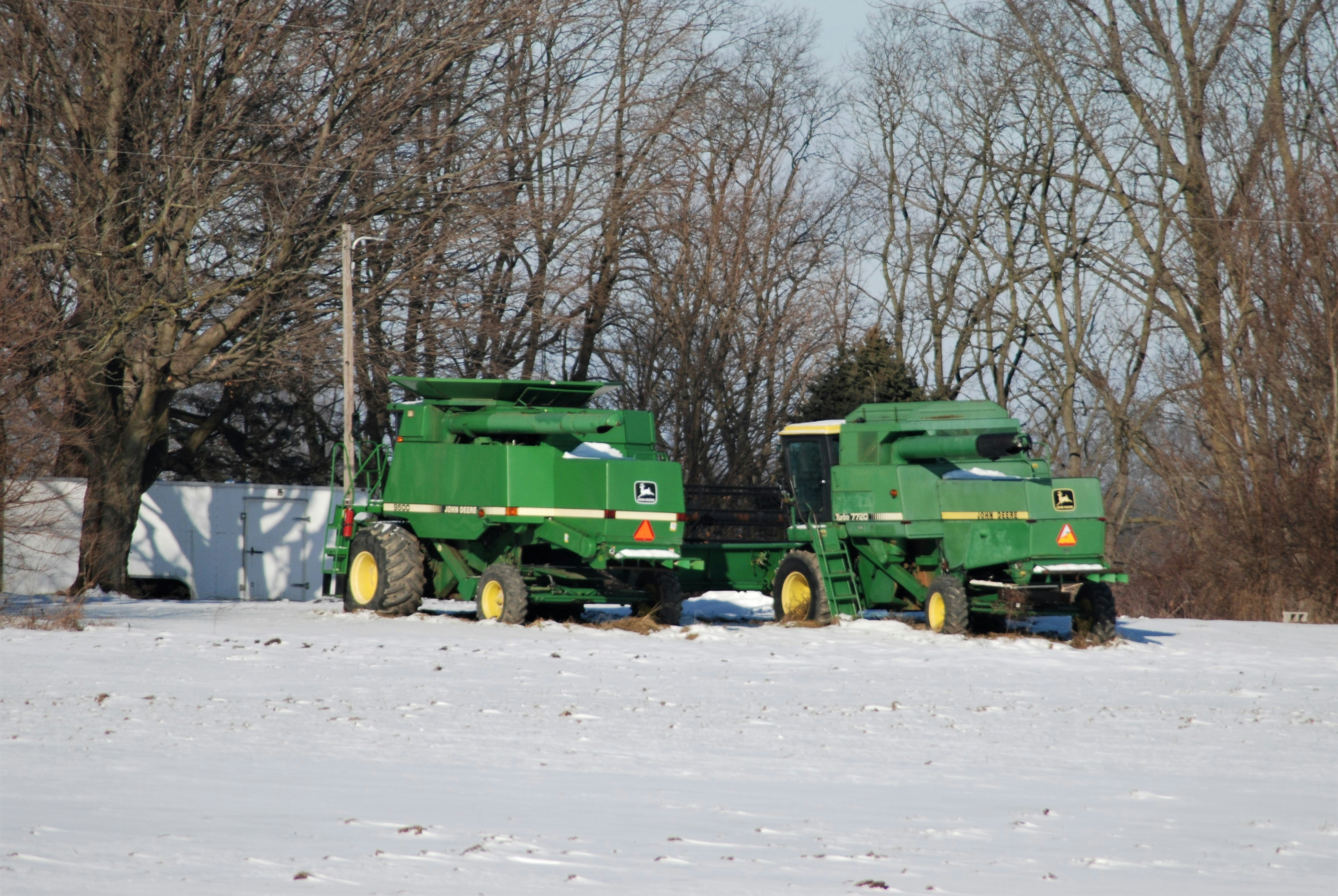 Green Harvesters Rest in Snowfield under Bare Winter Trees