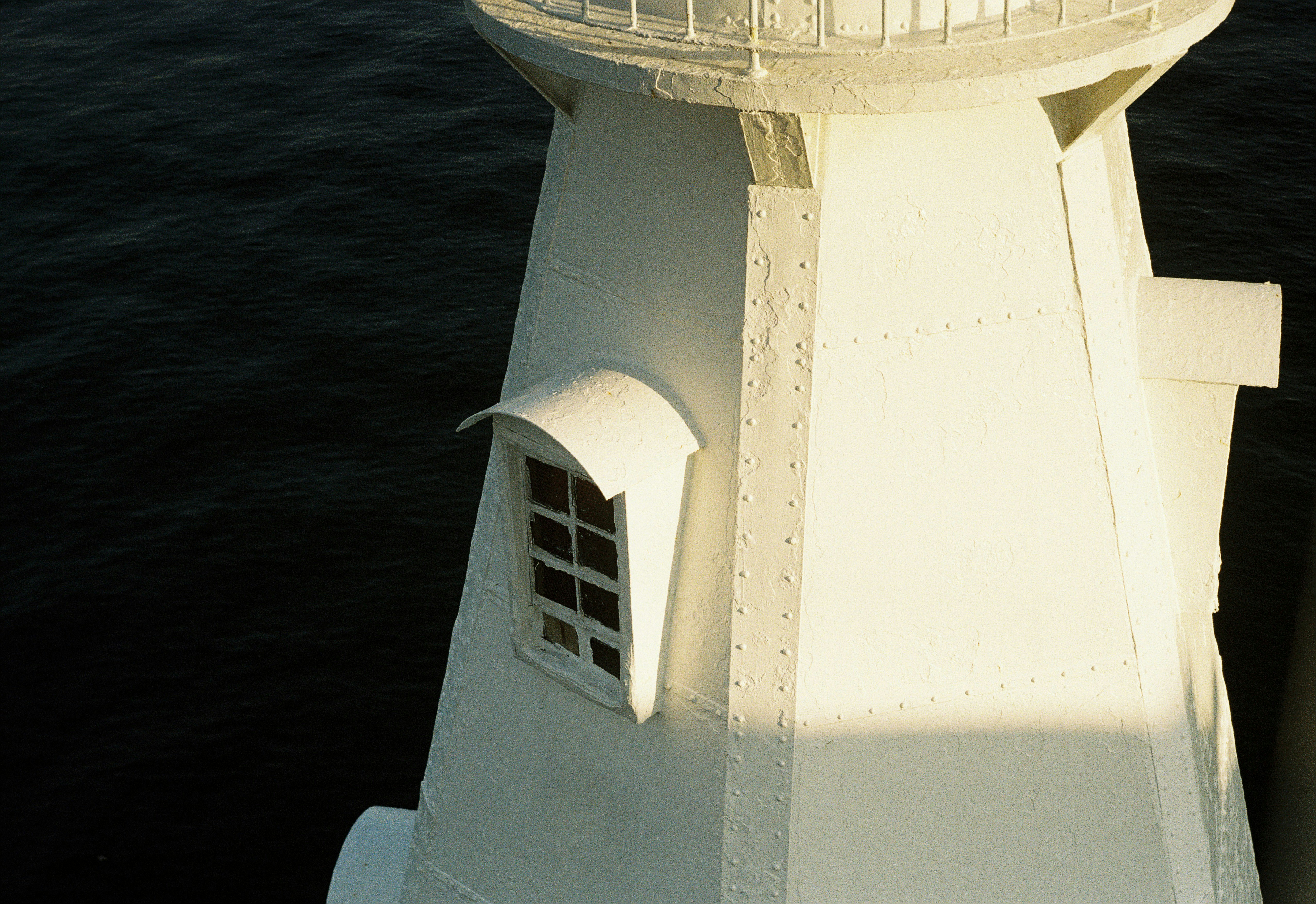 Sunlit Facade: A White Lighthouse Over Quiet Dark Waters