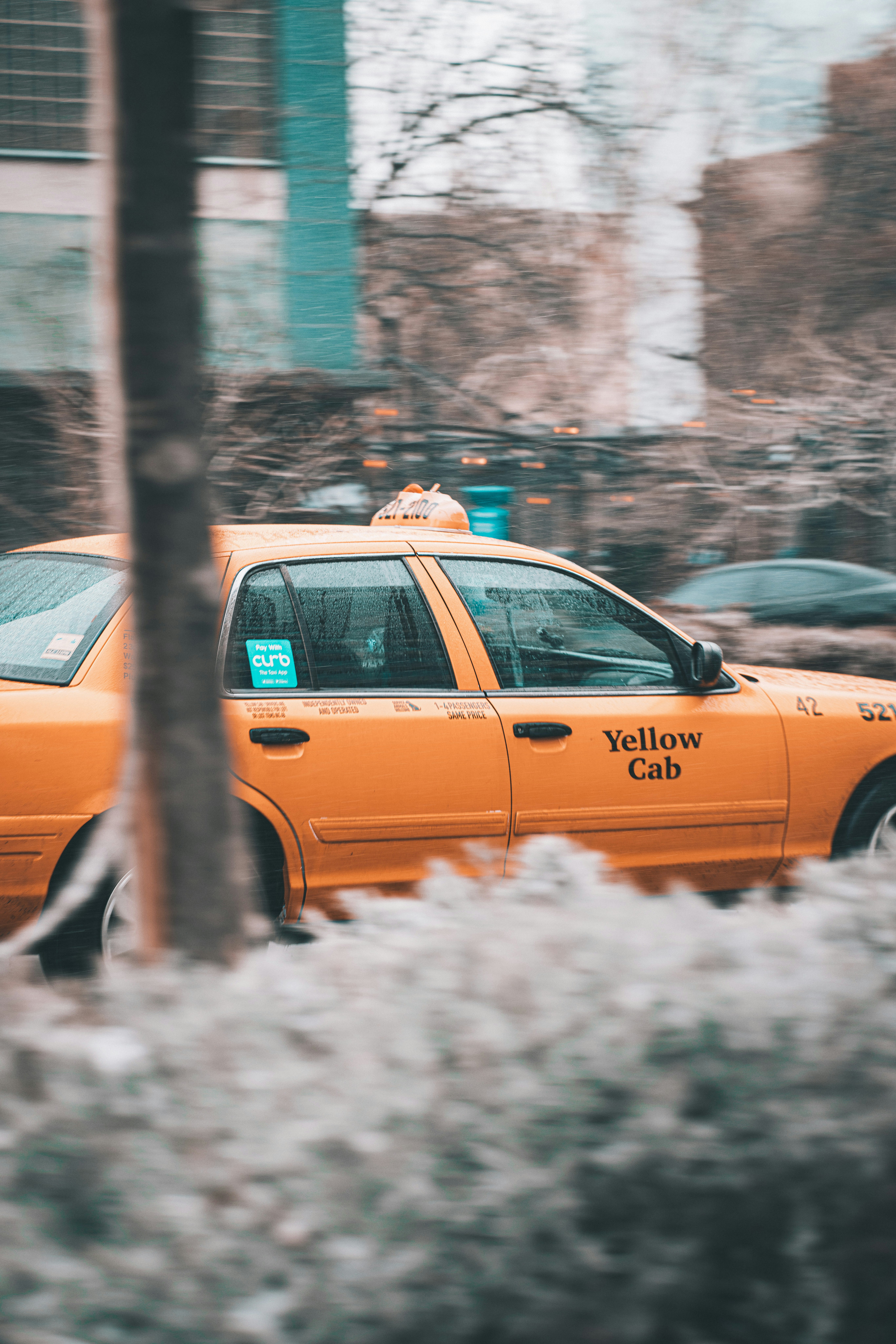 A yellow taxi cab driving down a street next to tall buildings photo ...