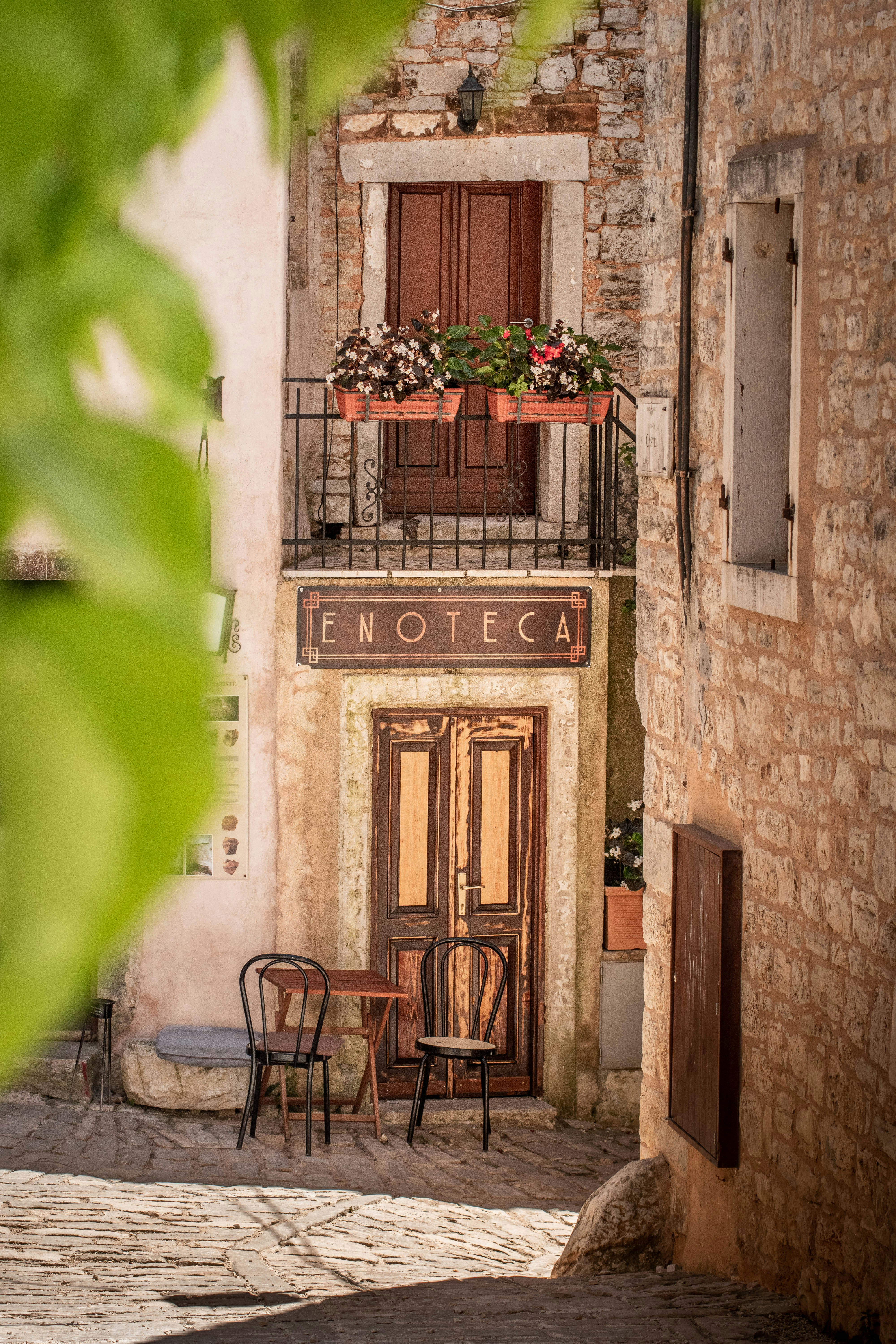 Balcony of Blooms Above Enoteca on a Sunlit Cobblestone Lane