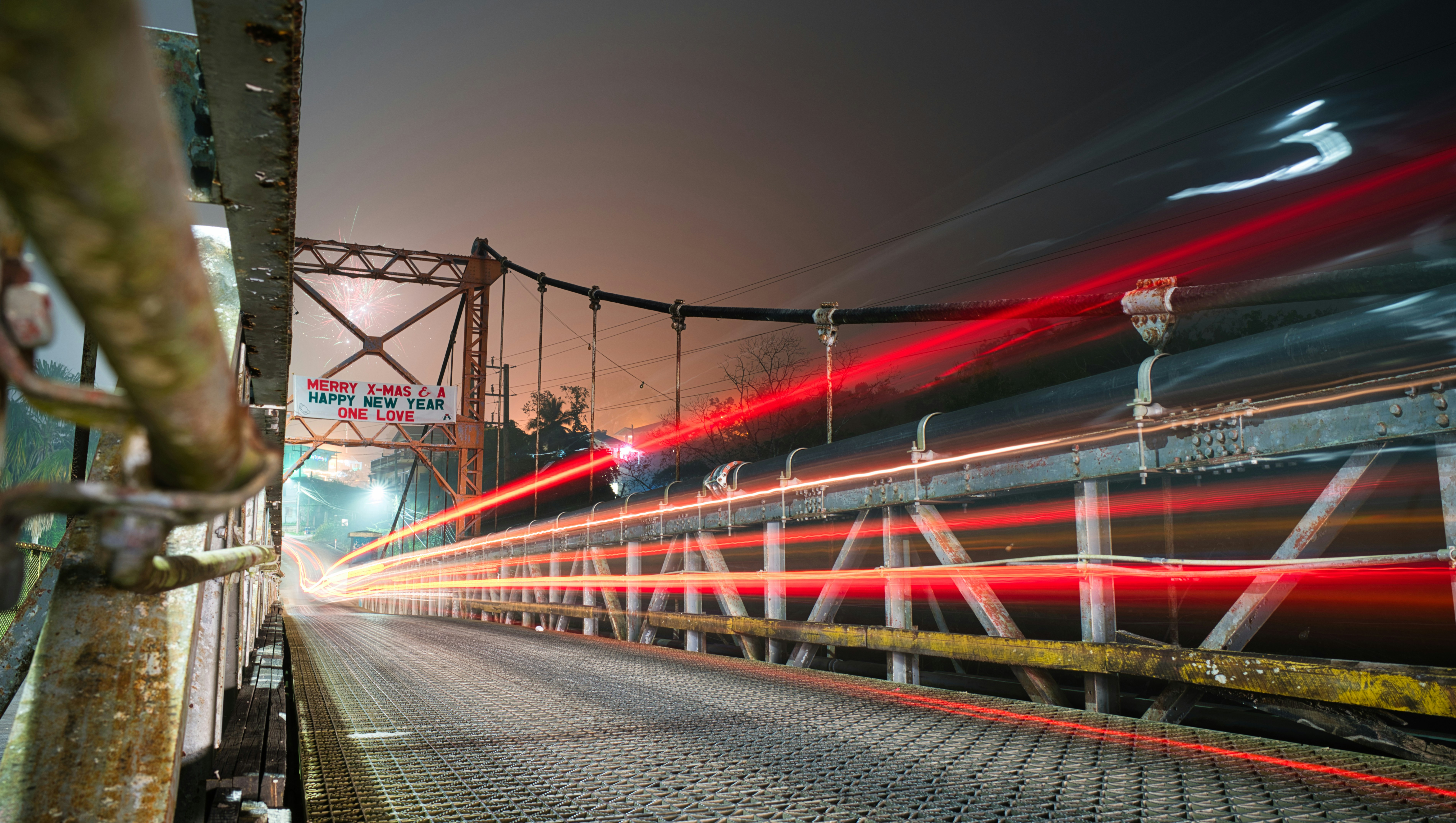 Long exposure of car lights creating vibrant trails over a historic bridge at night.